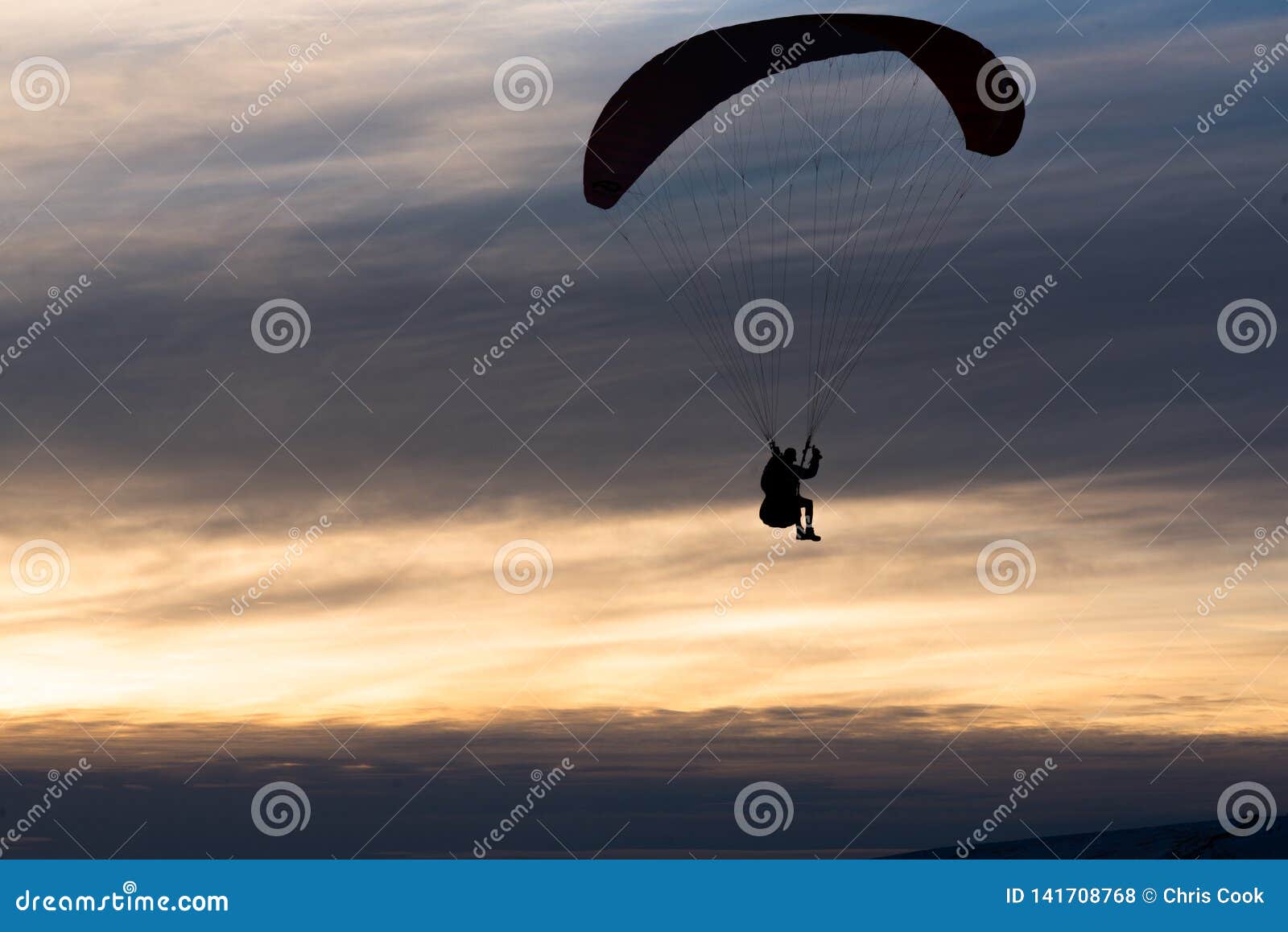 A Man Paragliding Down a Mountain Against a Cloudy Sunset in Winter ...