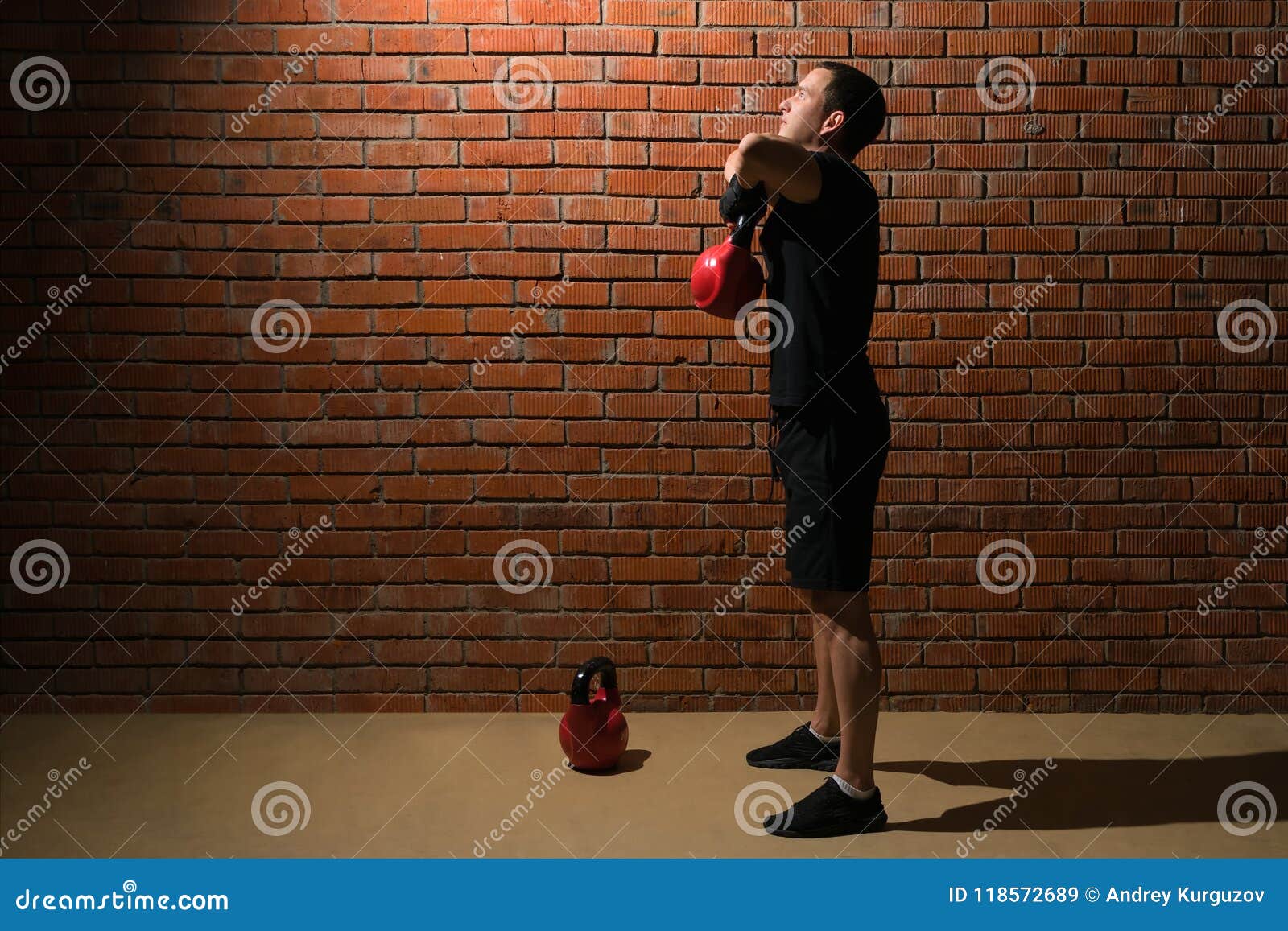 Man Performs an Exercise with a Red Dumbbell on a Brick Wall Background ...