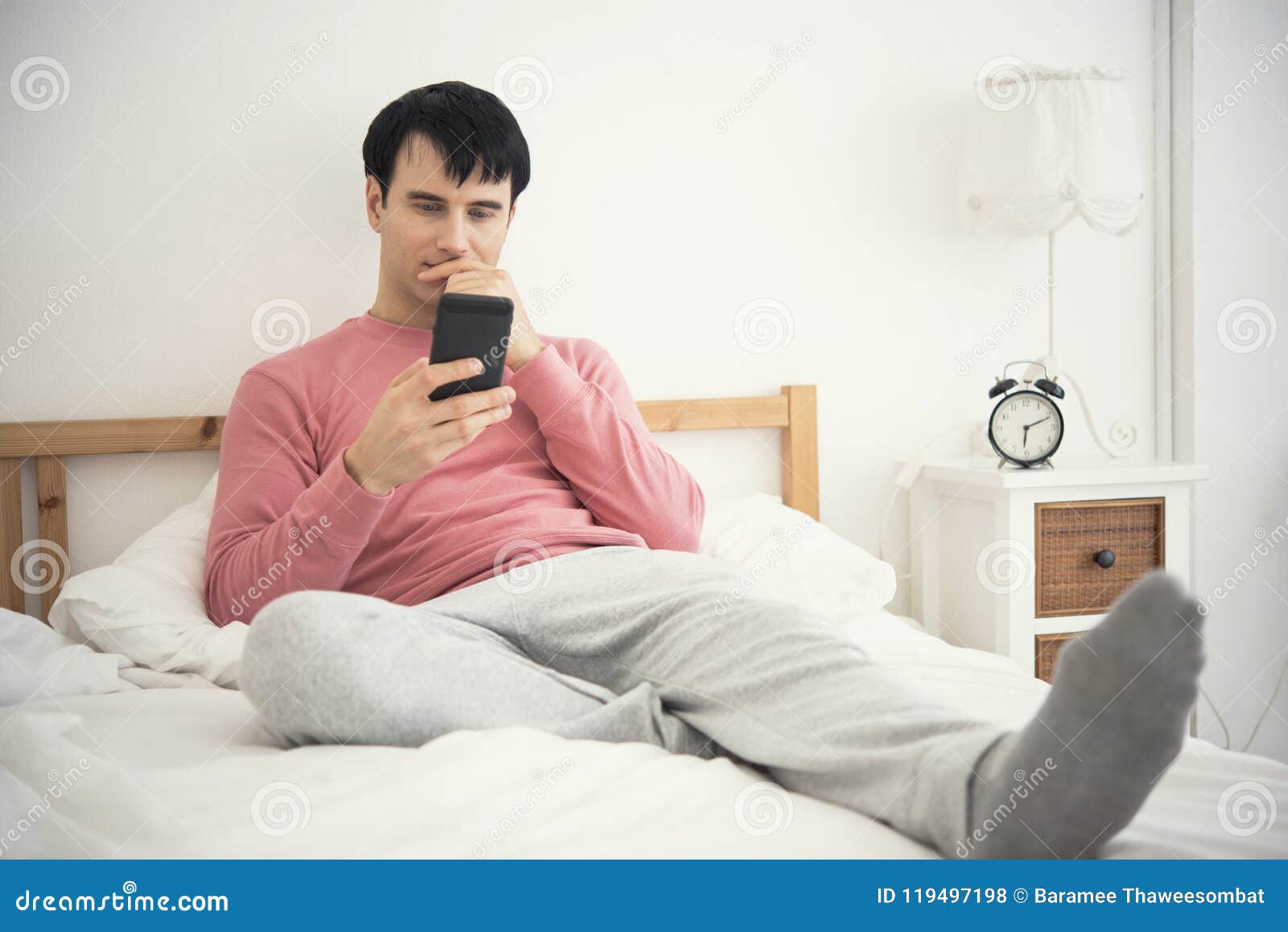 Man Playing Mobile Phone on Bed in Bedroom and Alarm Clock Stock Photo ...