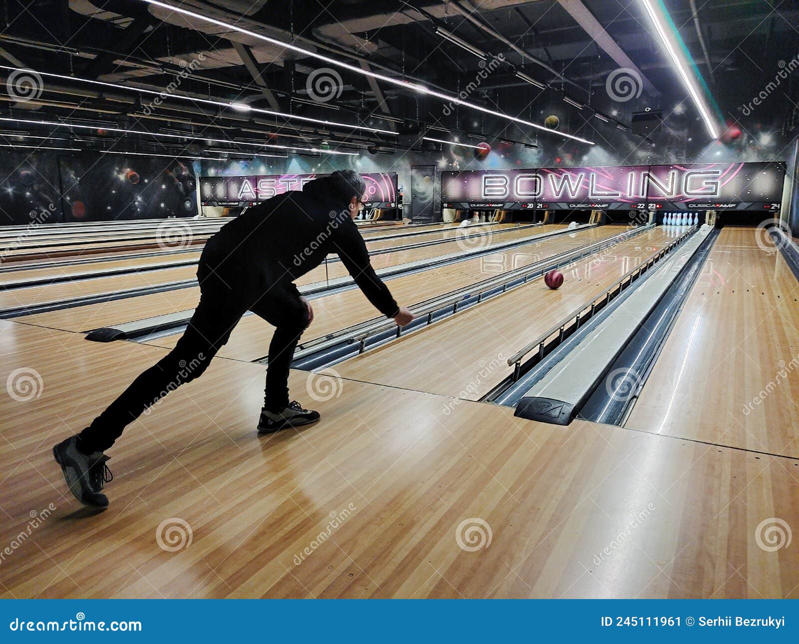 A Man Plays Bowling, Throws a Ball into the Skittles. Back View in ...