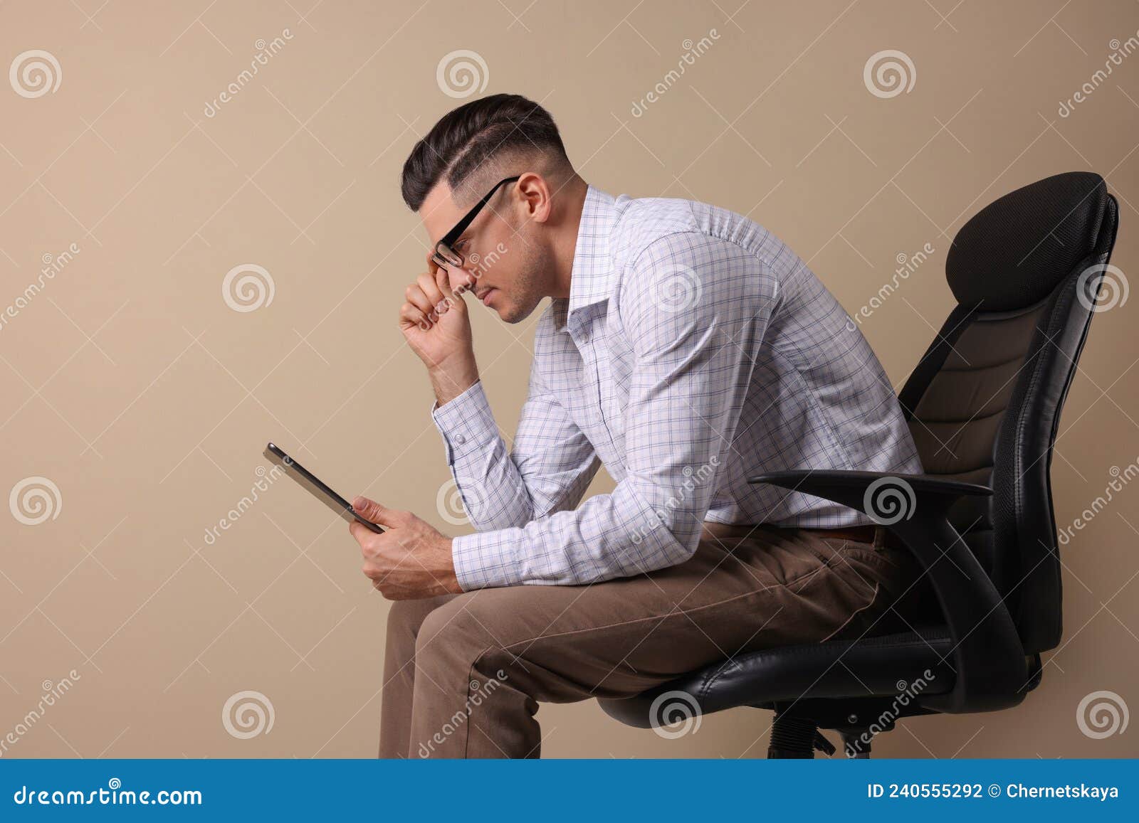 Man with Poor Posture Using Tablet while Sitting on Chair Against Beige ...
