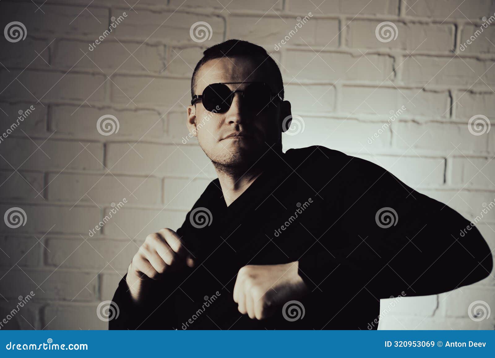 Man Posing Dramatically in Sunglasses Against White Brick Wall at Night ...