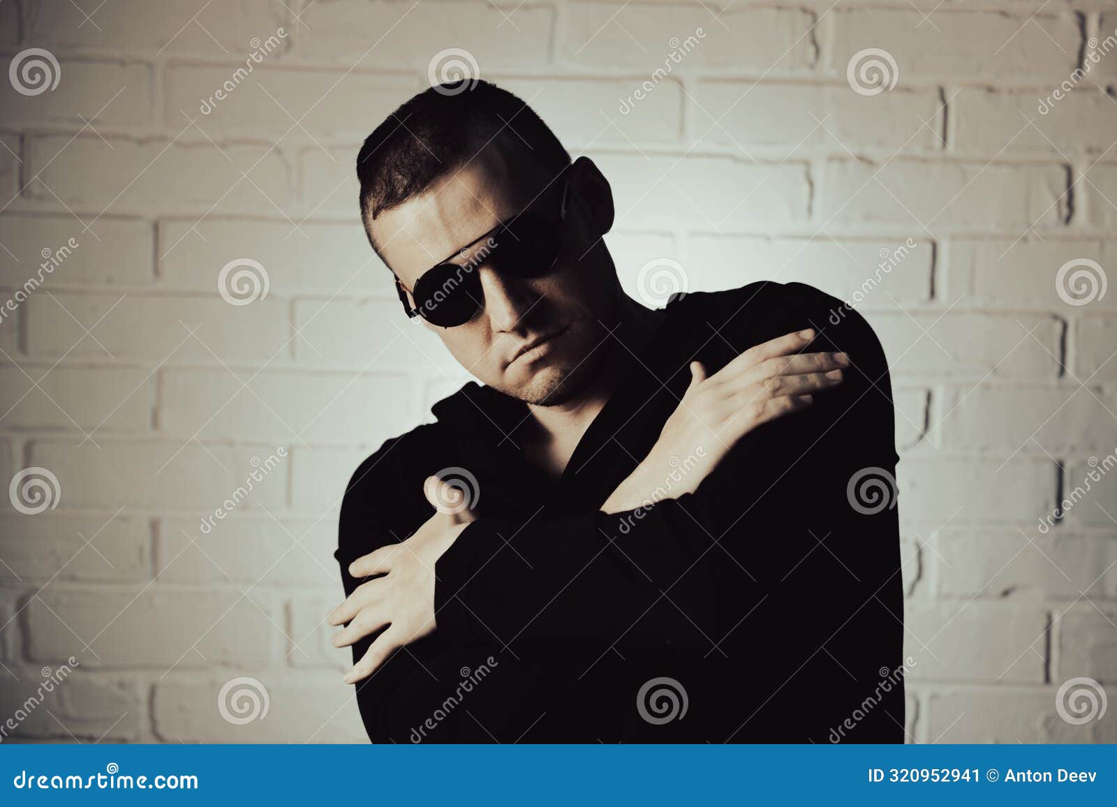 Man Posing Dramatically in Sunglasses Against White Brick Wall at Night ...