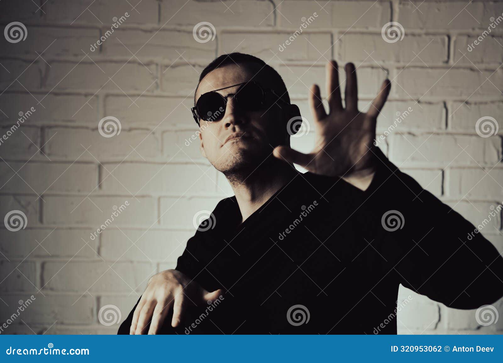 Man Posing Dramatically in Sunglasses Against White Brick Wall at Night ...