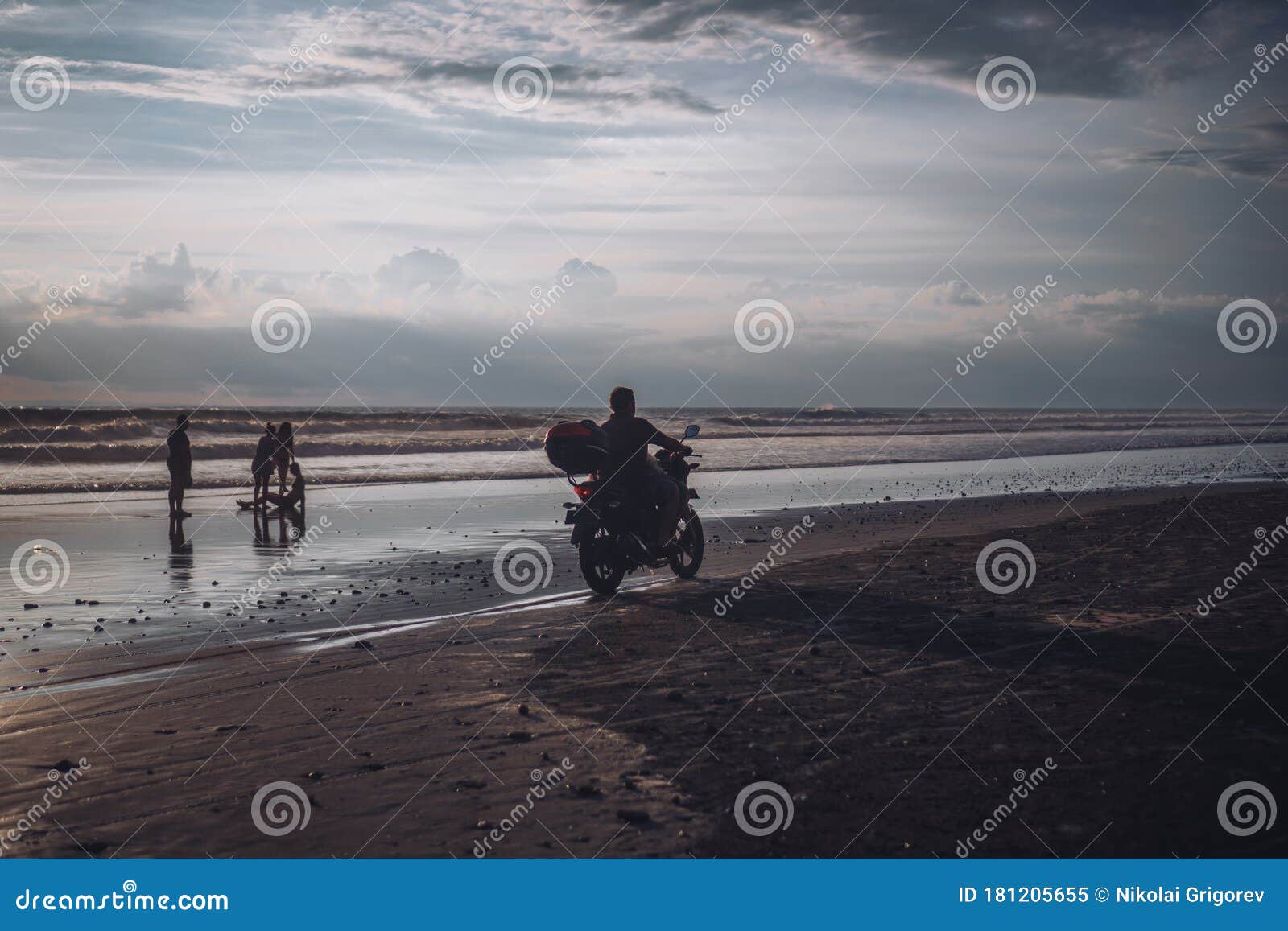 Man Riding a Motorcycle on a Beach with Black Sand and Clouds in the ...