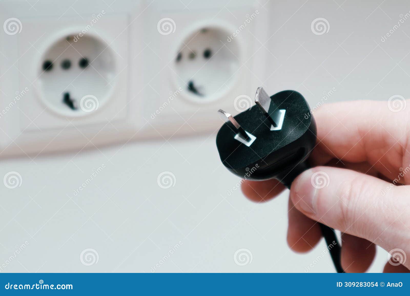 A Man S Hand Holds an Electrical Plug Next To the Sockets on the White ...