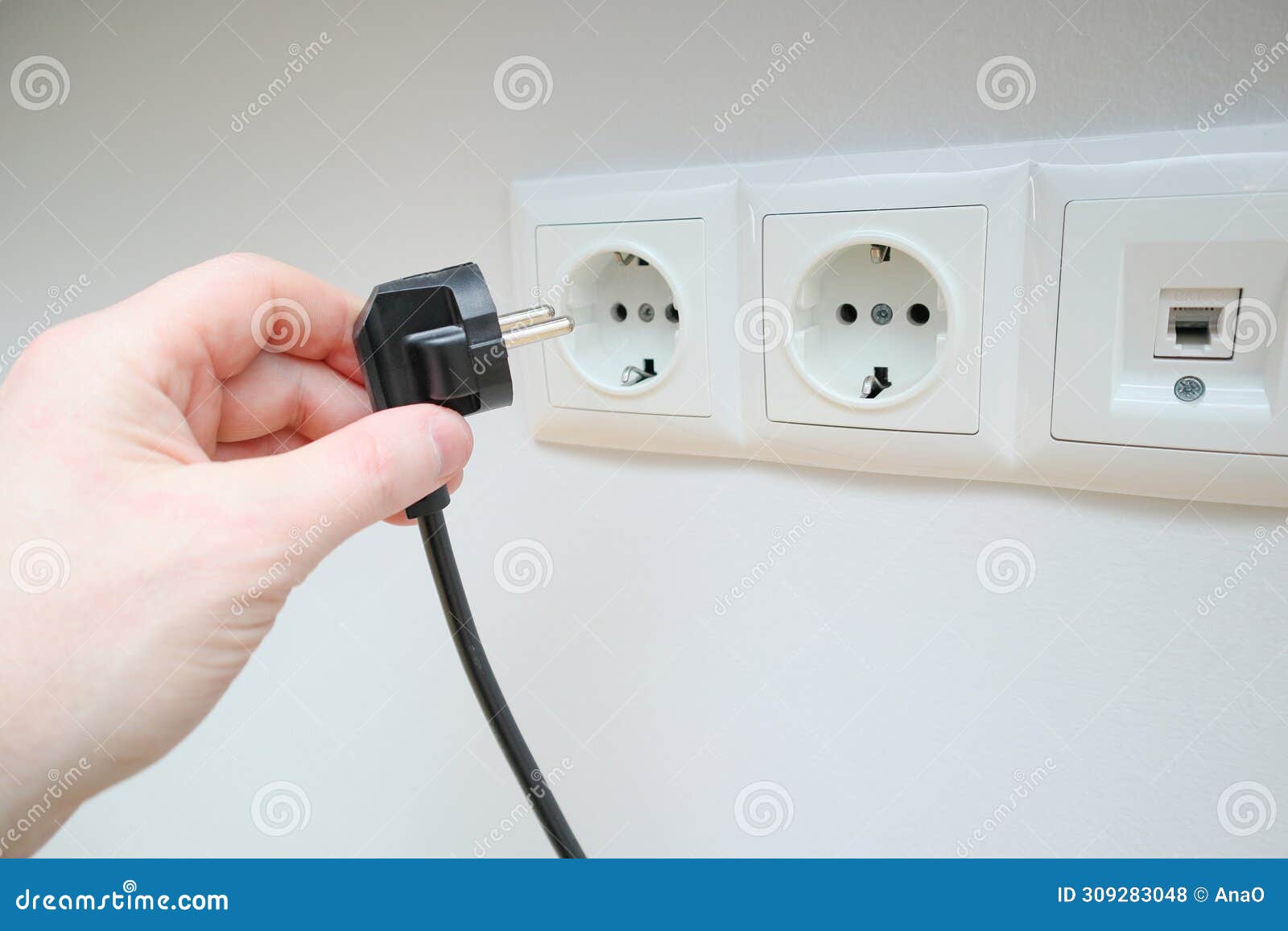 A Man S Hand Holds an Electrical Plug Next To the Sockets on the White ...
