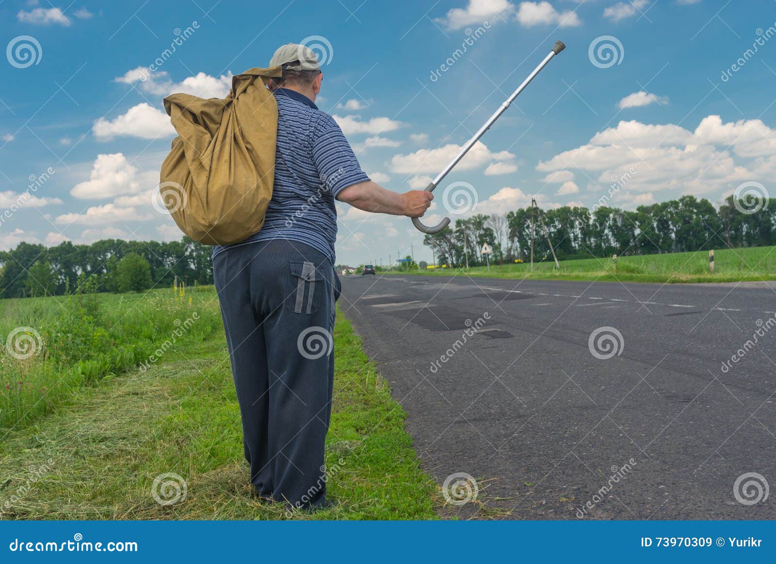 Man with Sack Standing on a Roadside Holding Walking Stick Up Stock ...