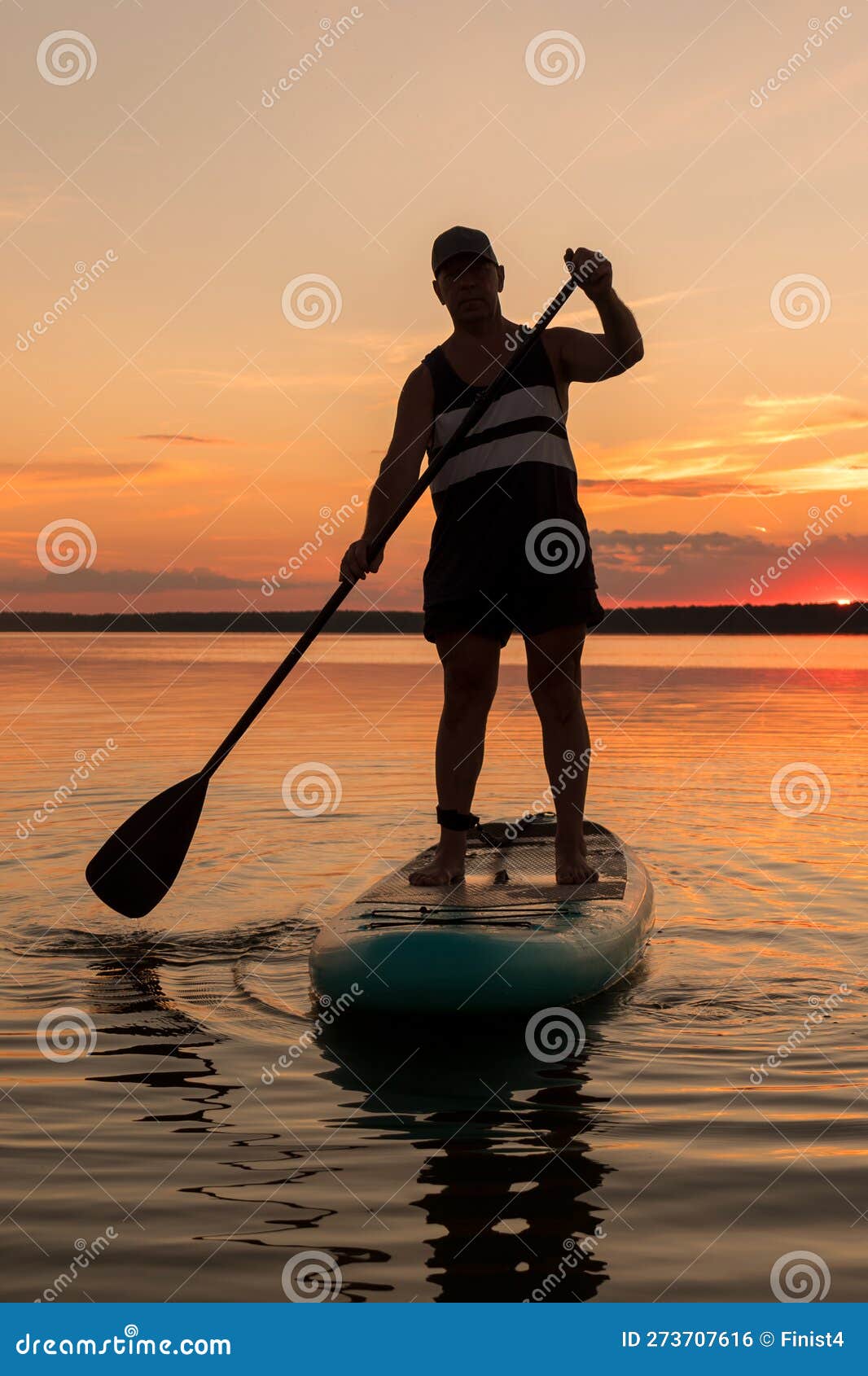 A Man In Shorts Stands On A Sup Board In The Evening At Sunset In The