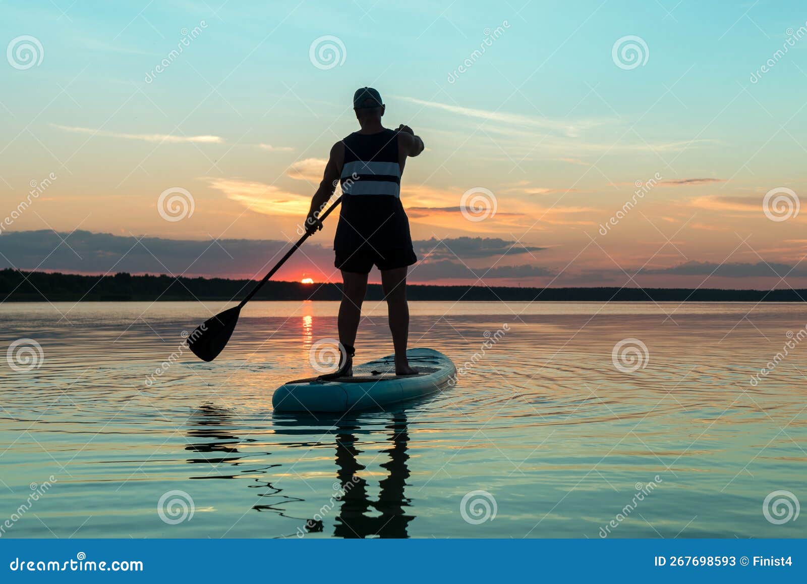 A Man In Shorts Stands On A Sup Board With An Oar At Sunset In A Lake