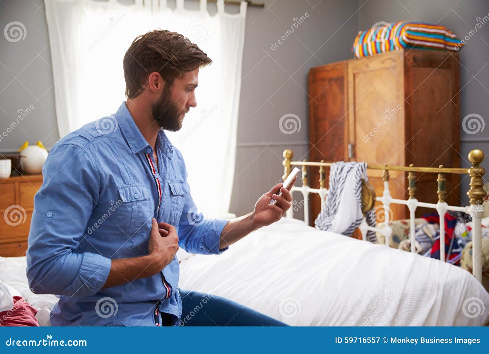 Man Sitting on Bed Getting Dressed and Checking Mobile Phone Stock ...
