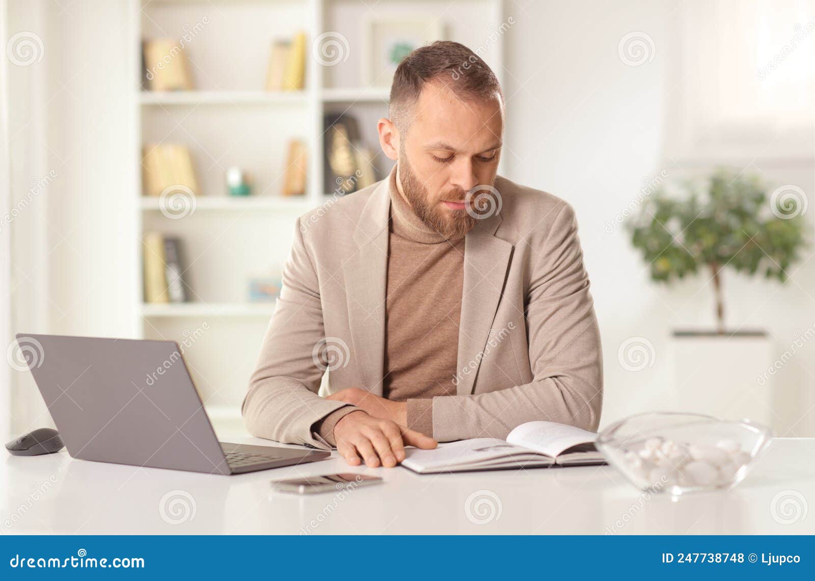 Man Sitting at a Desk with a Laptop Computer and Reading a Book Stock ...