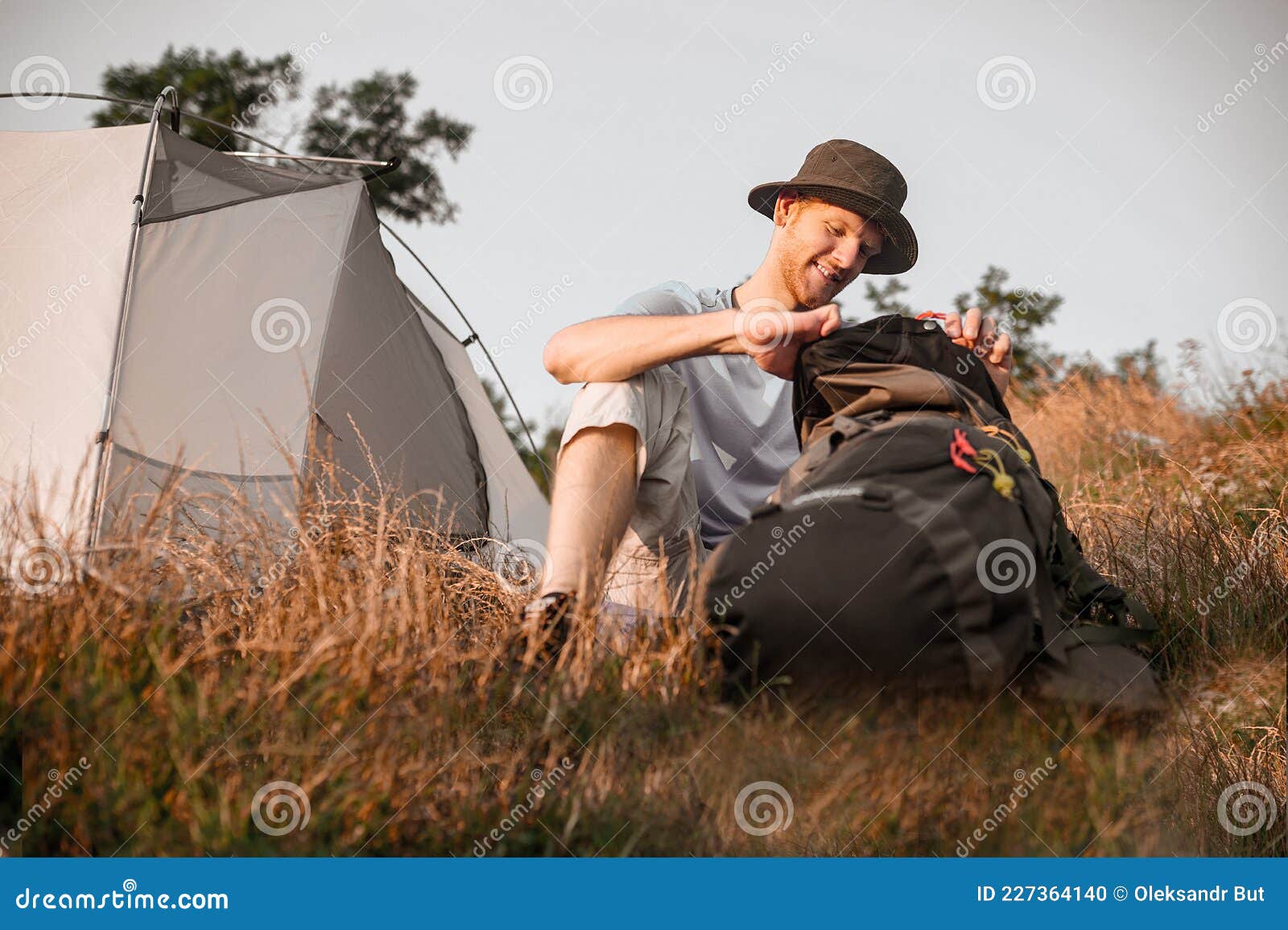 A Man Sitting on the Ground and Packing His Backpack Stock Photo ...