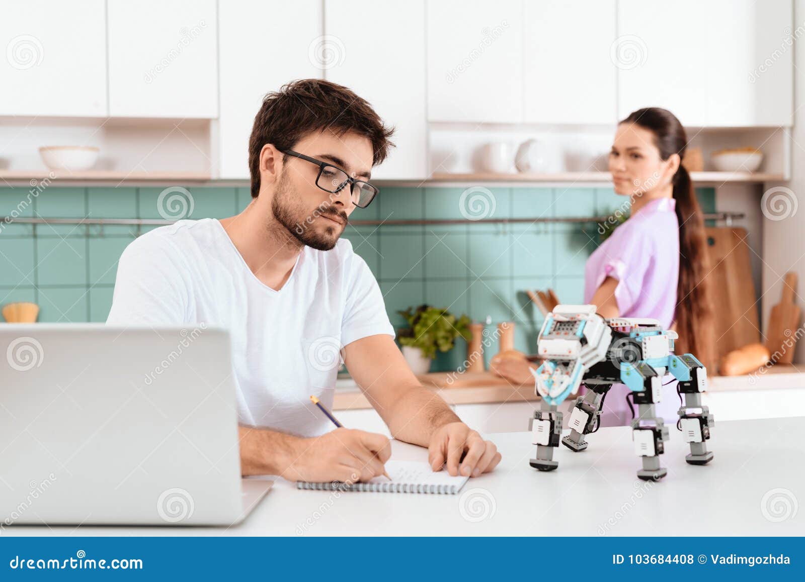 A Man is Sitting at the Kitchen Table and Programming a Robot. the ...