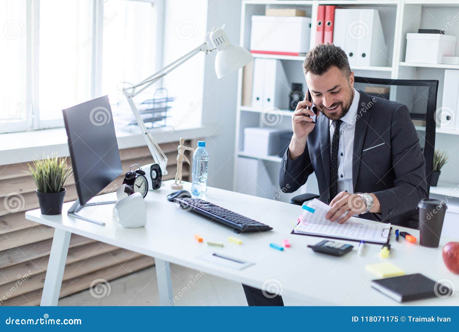 A Man is Sitting in the Office at the Table, Talking on the Phone and ...