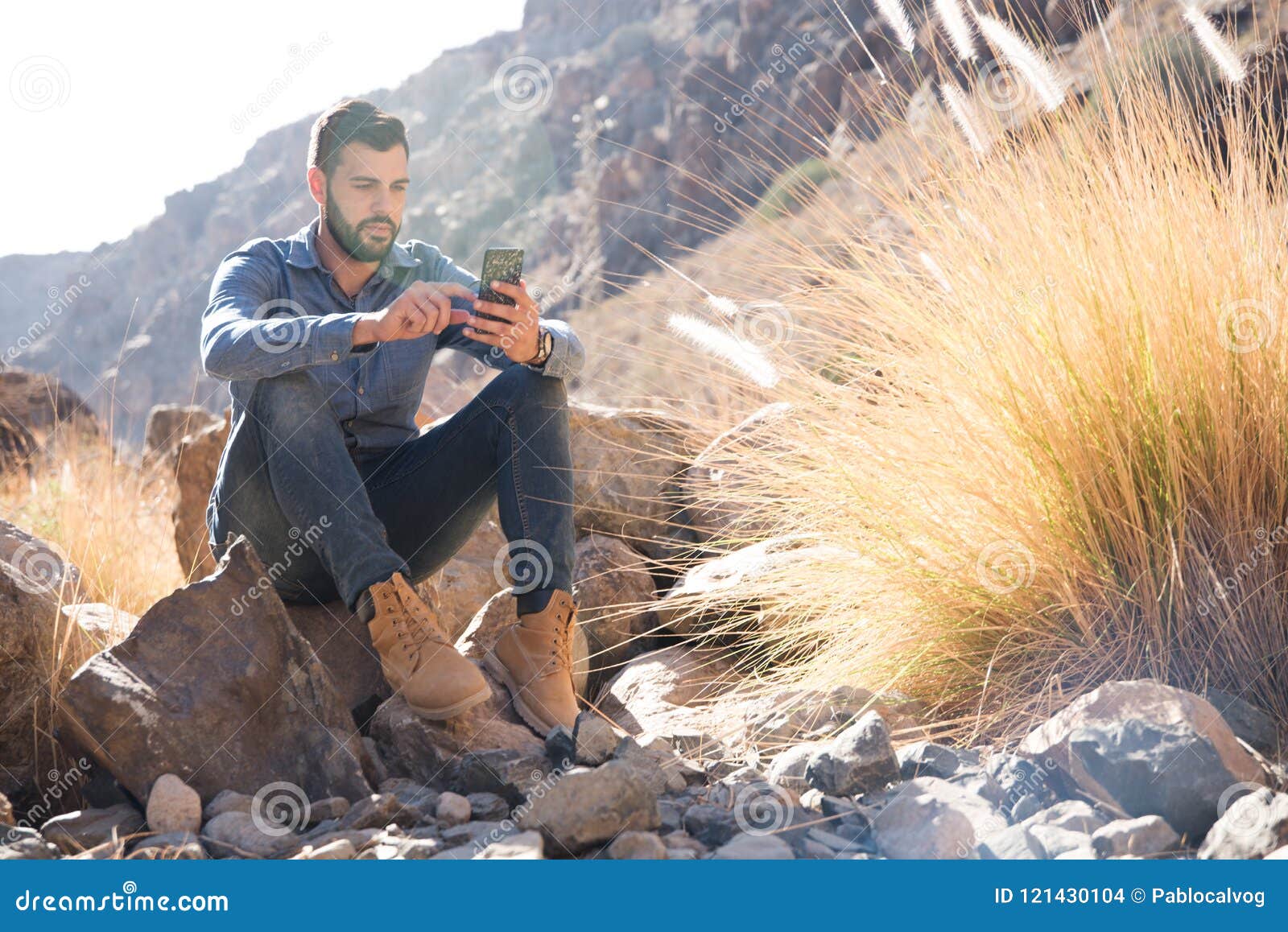 Man Sitting on a Rock Texting on a Cell Phone Stock Photo - Image of ...