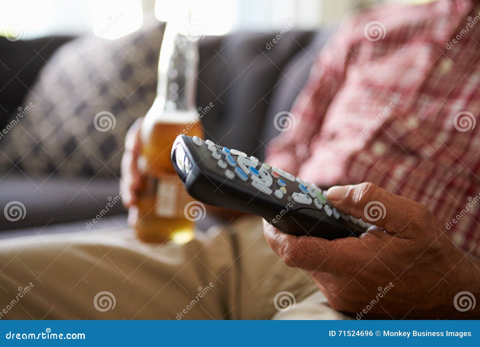 Man Sitting on Sofa Holding TV Remote and Bottle of Beer Stock Photo ...