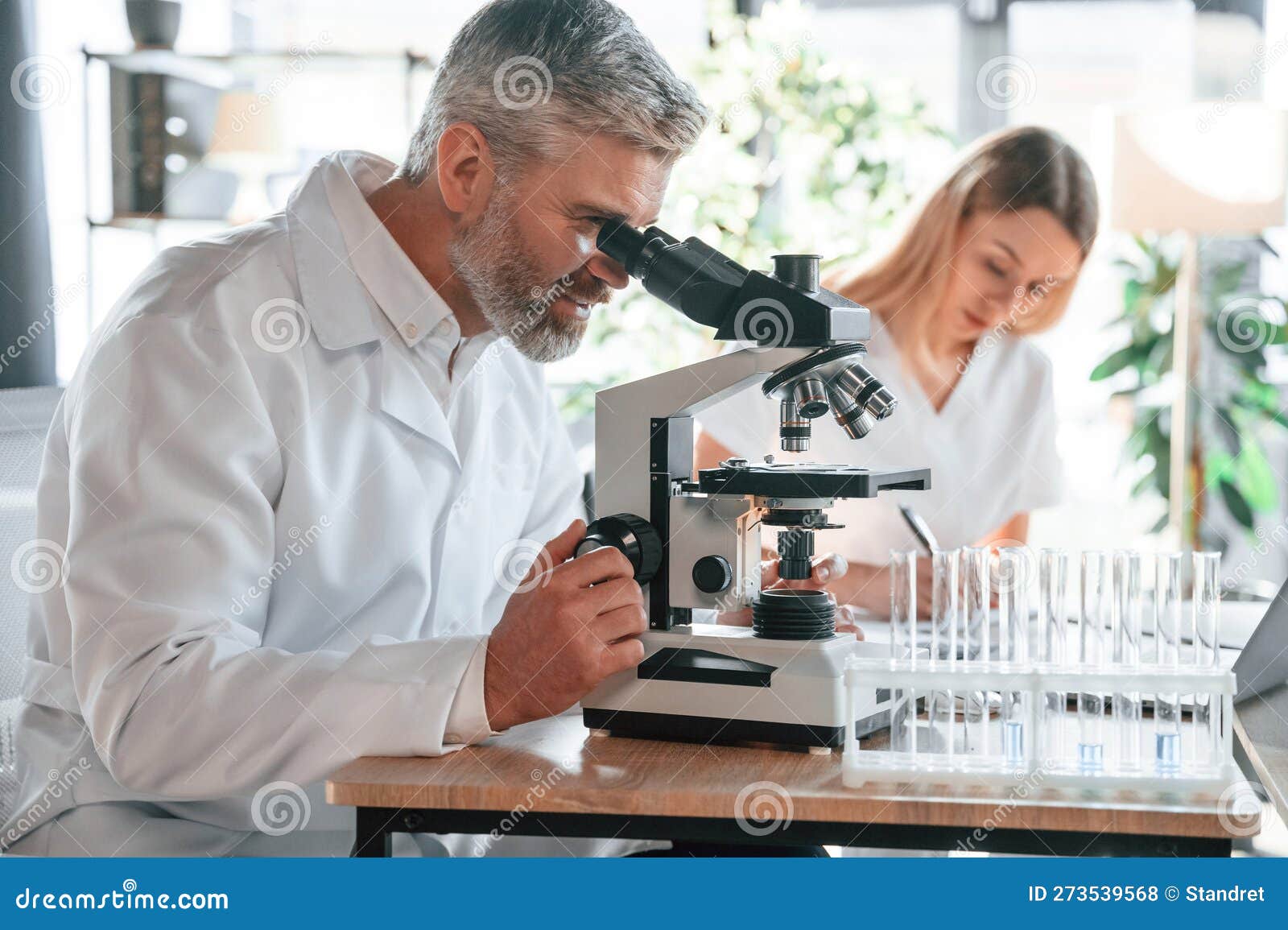 Man is Sitting and Using Microscope. Two Clinic Workers are Indoors ...