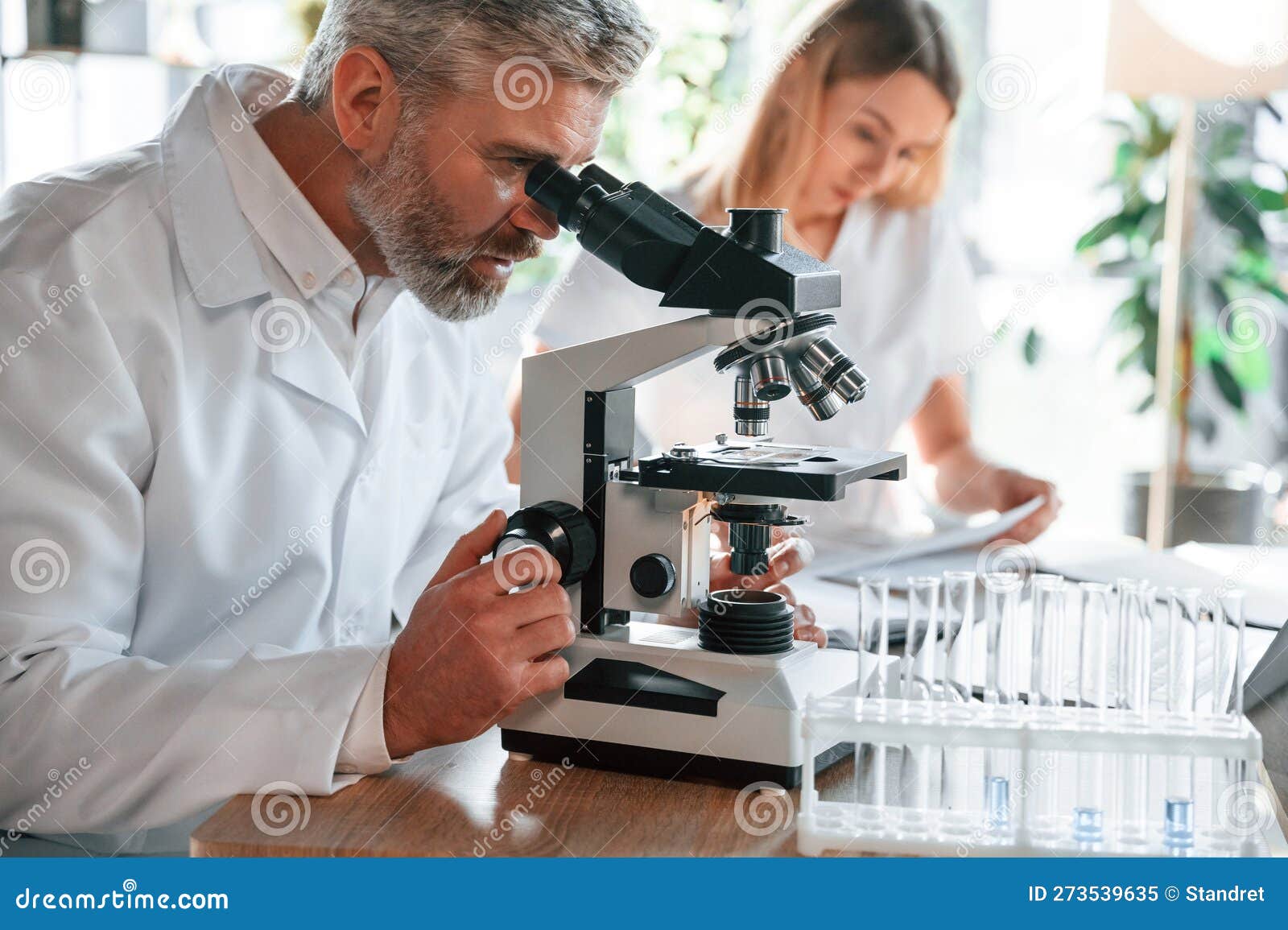 Man is Sitting and Using Microscope. Two Clinic Workers are Indoors ...
