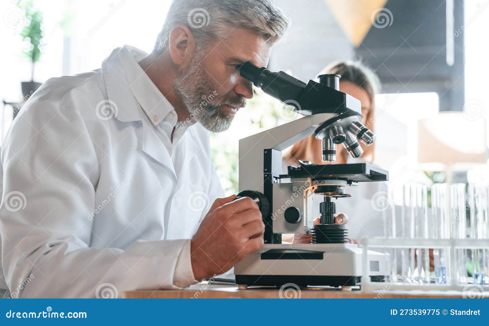Man is Sitting and Using Microscope. Two Clinic Workers are Indoors ...