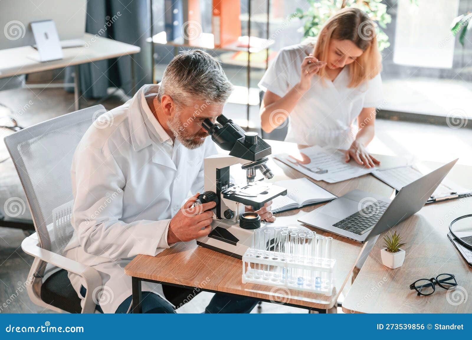 Man is Sitting and Using Microscope. Two Clinic Workers are Indoors ...