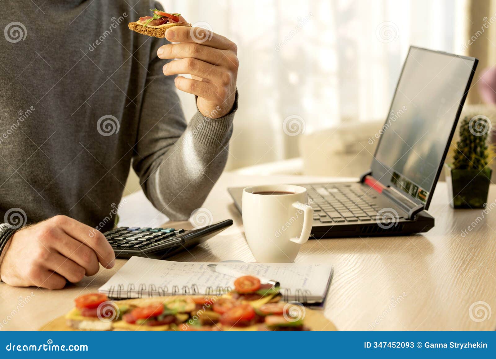 Man Snacking on Sandwich and Coffee while Working at Table in Office ...