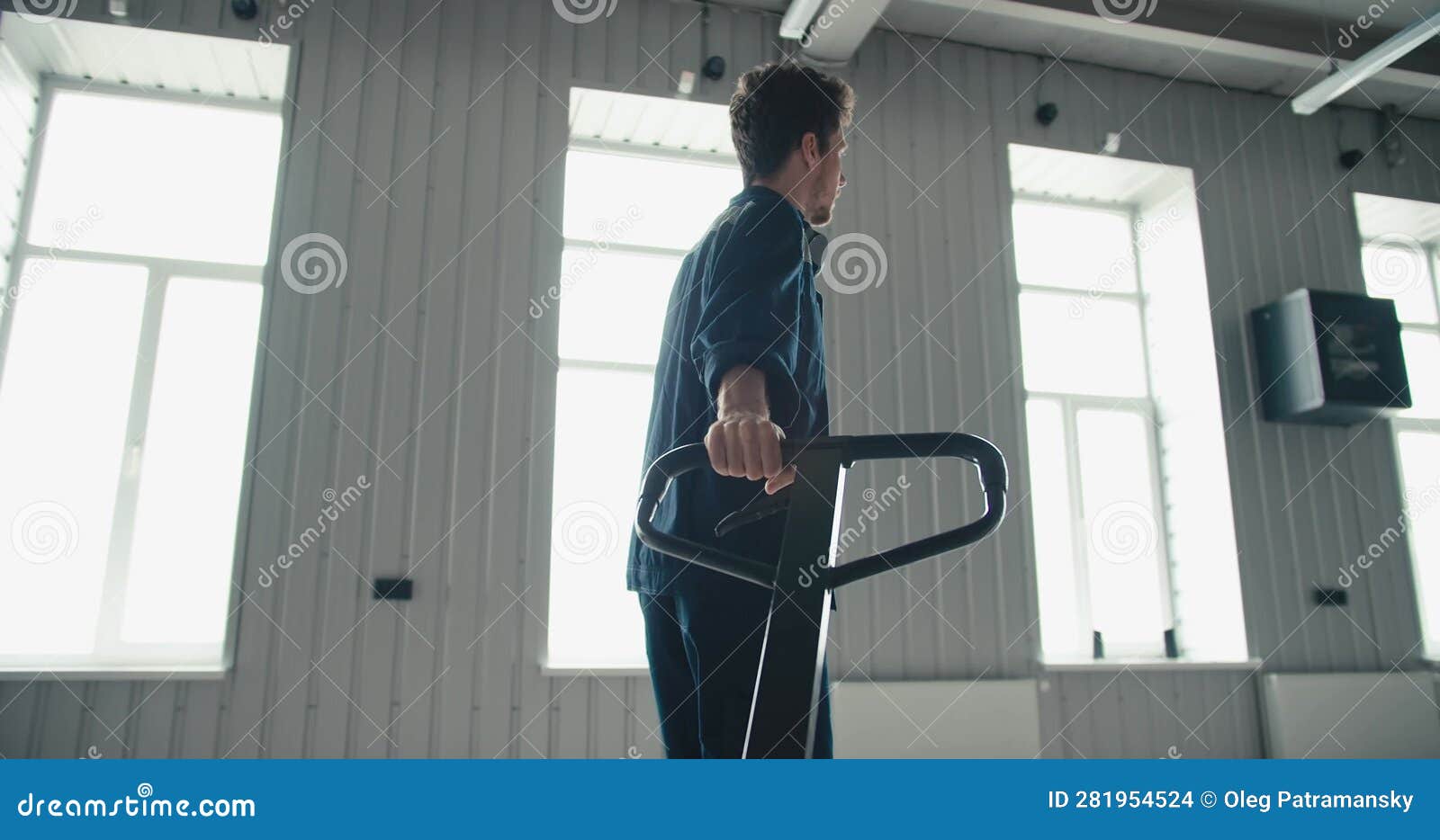 A Man in a Special Blue Uniform Pulls a Load in a Warehouse by the ...