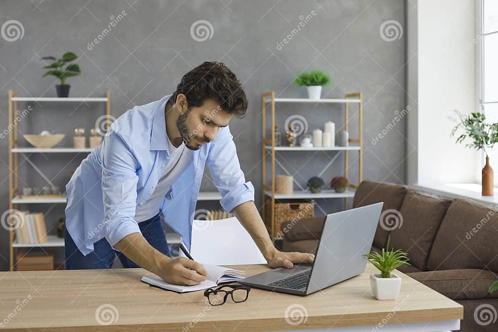 Man Standing by Desk, Using Laptop Computer and Writing Down ...