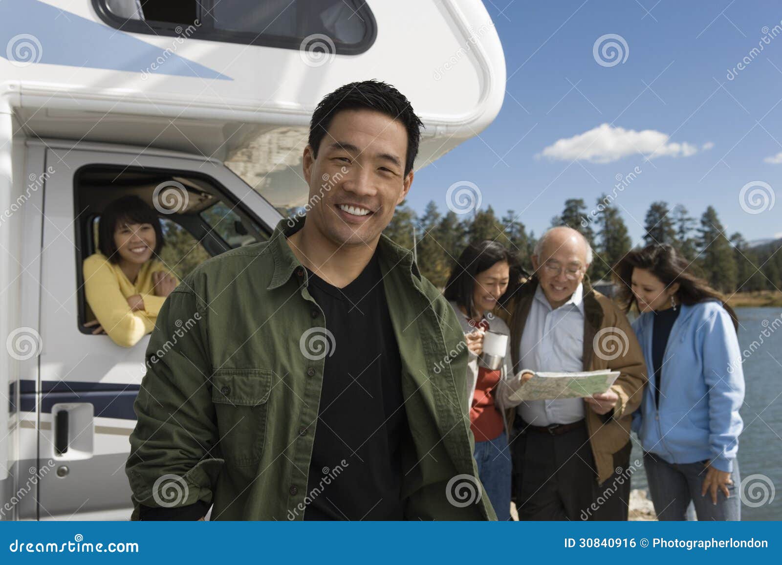 Man Standing in Front of RV at Lake with Family Behind Stock Photo ...