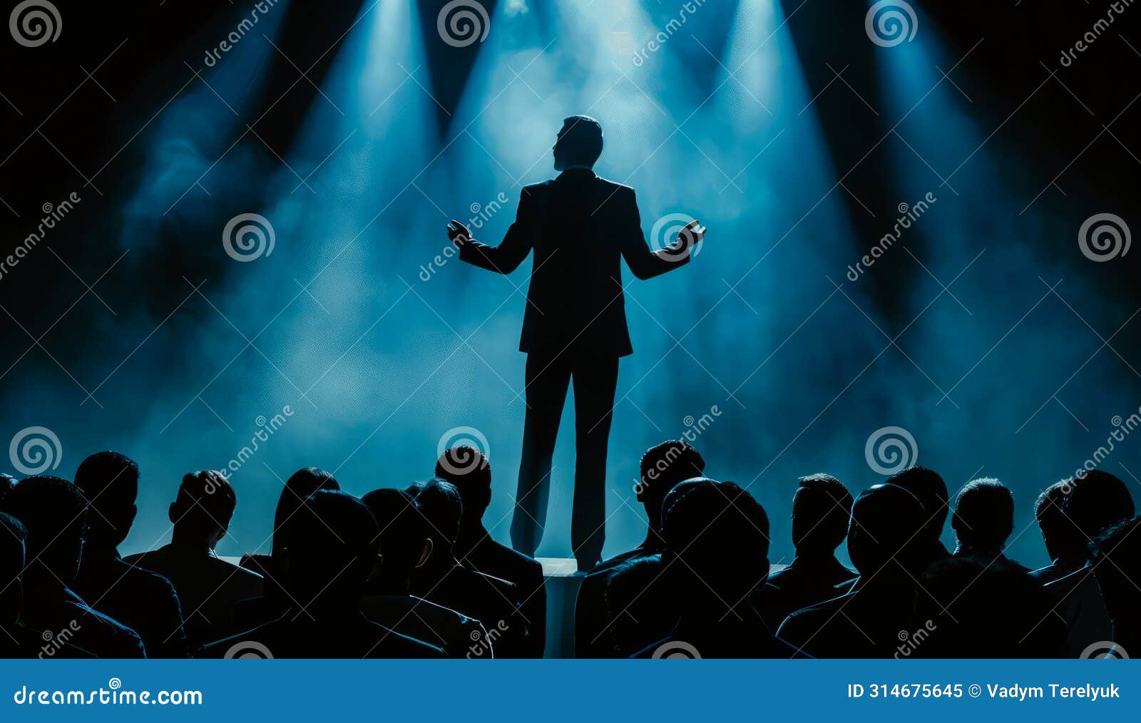 A Man Stands on a Stage in Front of a Crowd of People. he is Giving a ...