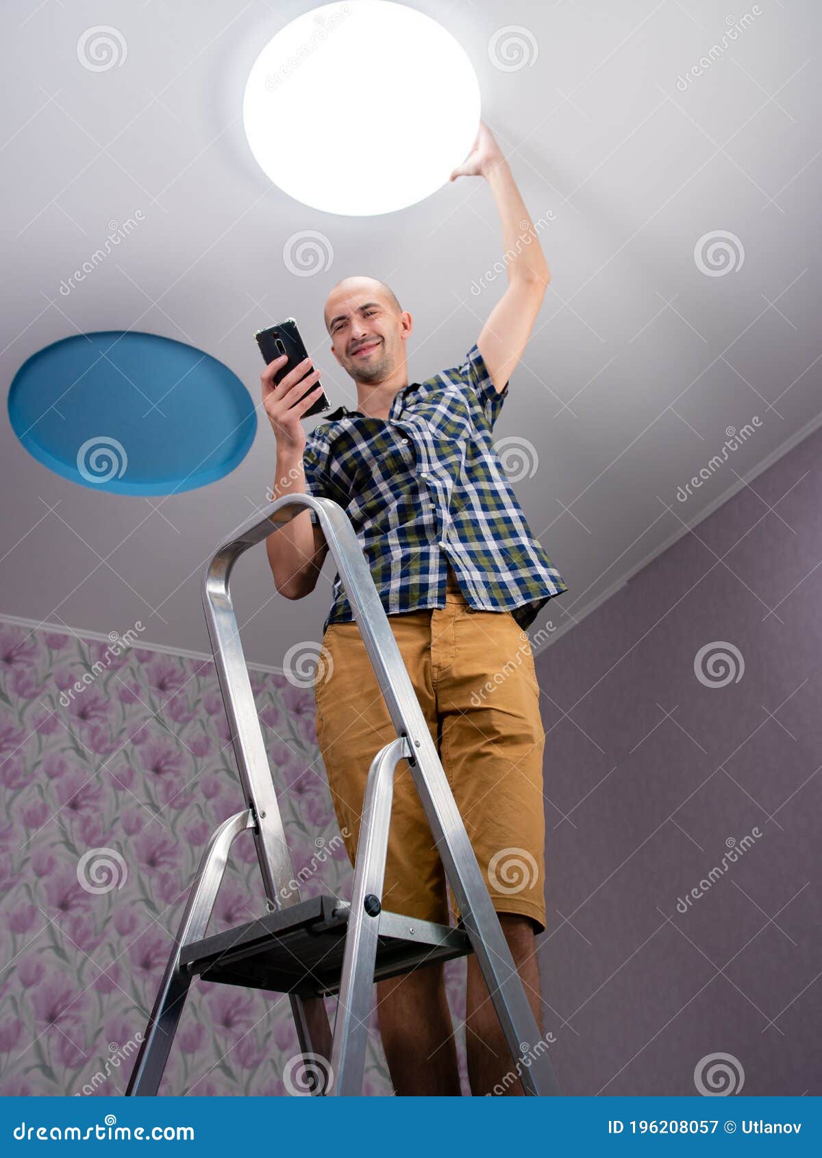 A Man Uses an App on His Smartphone To Control a Smart Ceiling Light ...