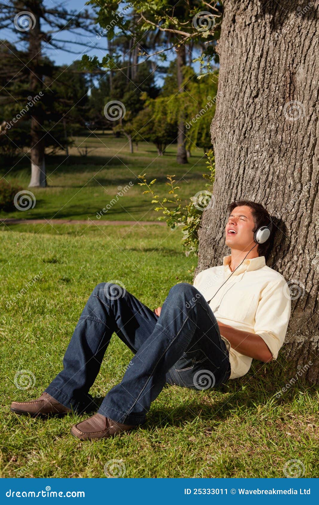 Man Using Headphones To Sing Along To Music while Resting a Tree Stock ...