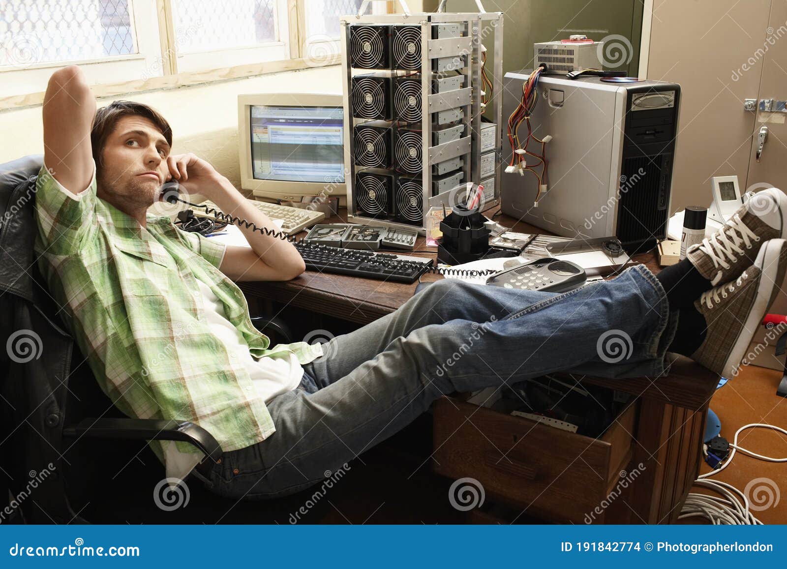 Man Using Phone Surrounded by Computer Equipment with Feet Up on Desk ...