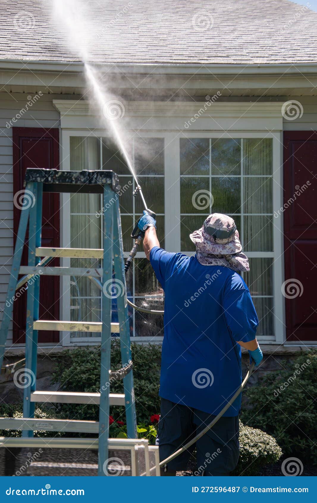 A Man Using a Power Washer To Clean the Windows and Front of a House ...