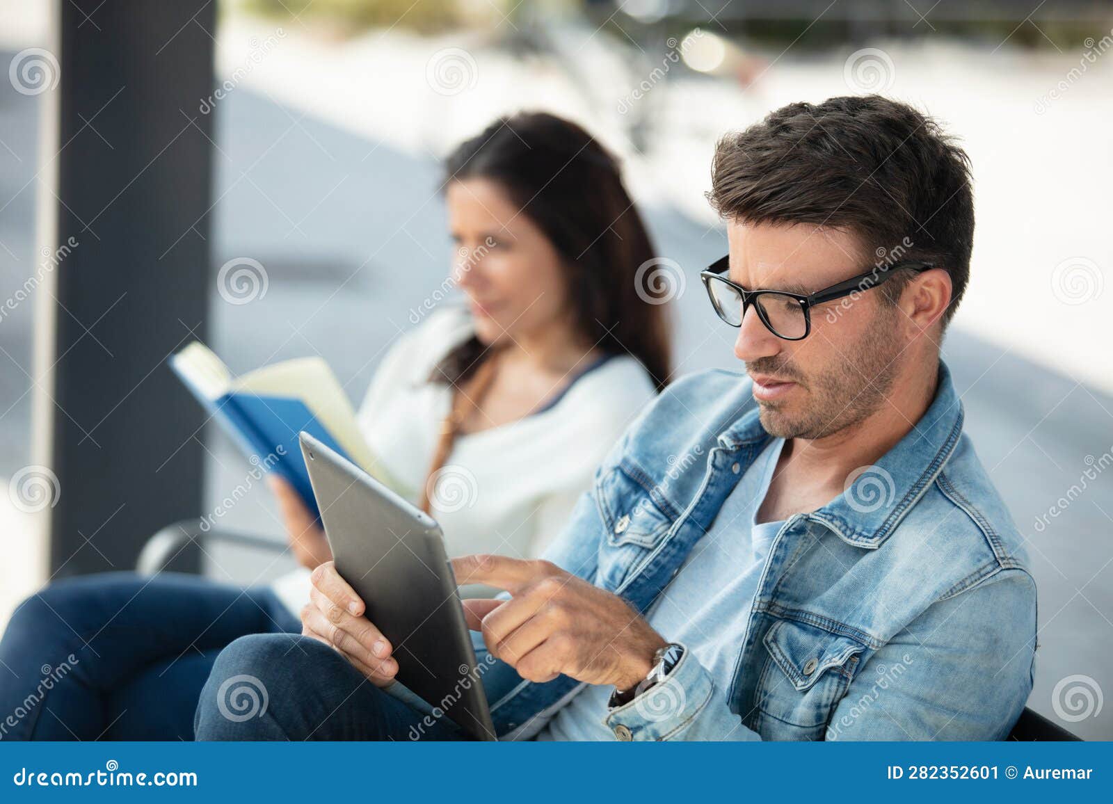 Man Using Tablet and Woman Reading Book at Bus-stop Stock Image - Image ...