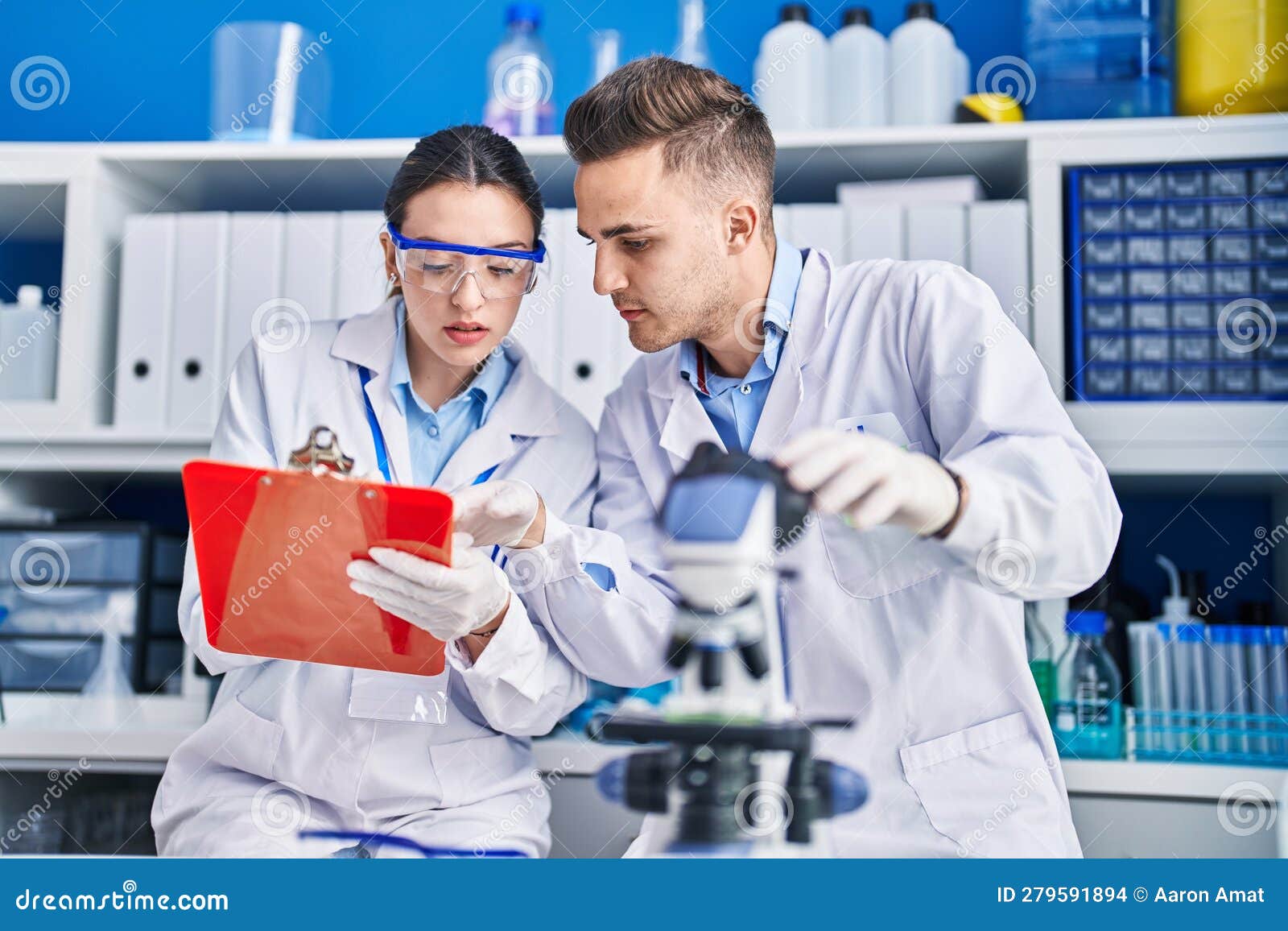 Man and Woman Scientists Using Microscope Write on Clipboard at ...