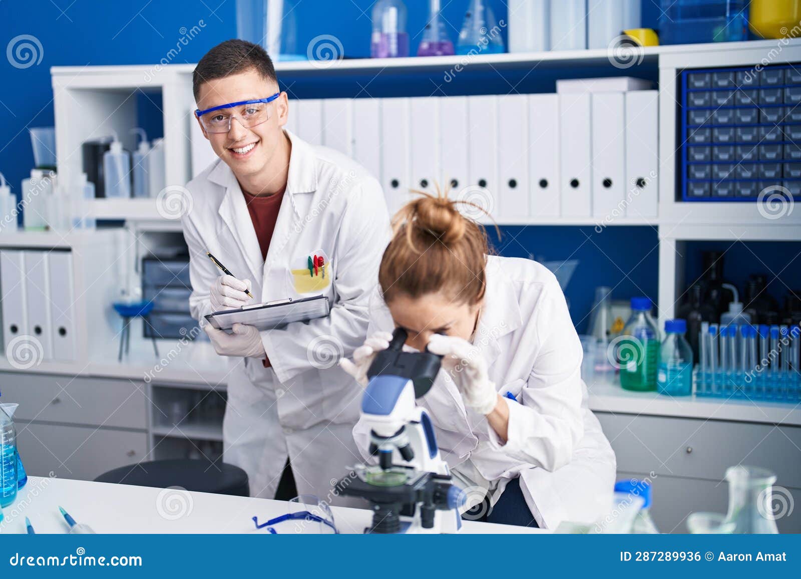 Man and Woman Scientists Using Microscope Write on Document at ...