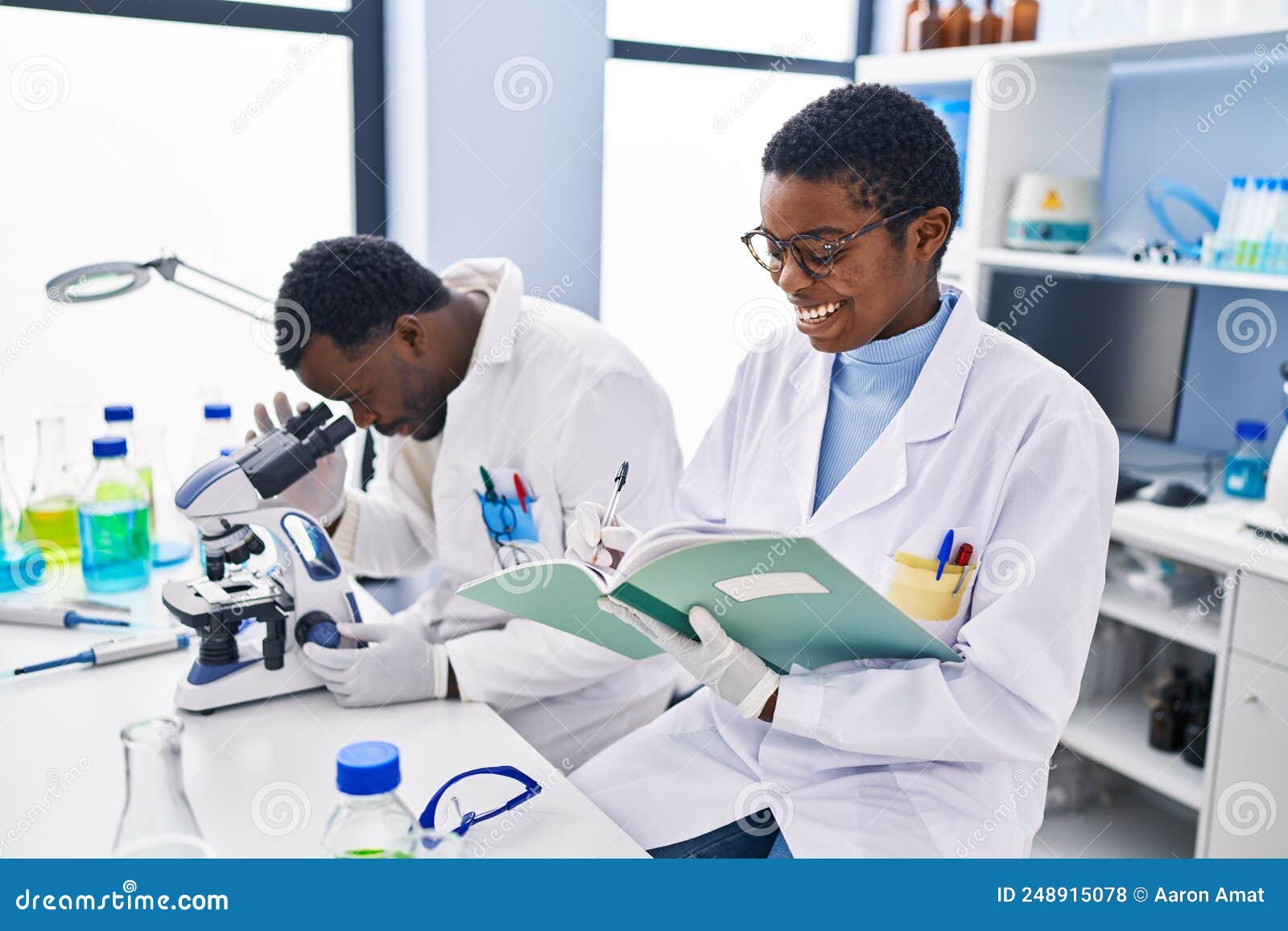 Man and Woman Scientists Using Microscope Writing on Notebook at ...