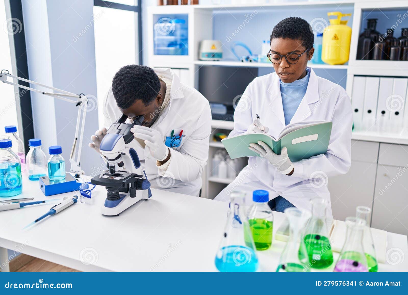 Man and Woman Scientists Using Microscope Writing on Notebook at ...
