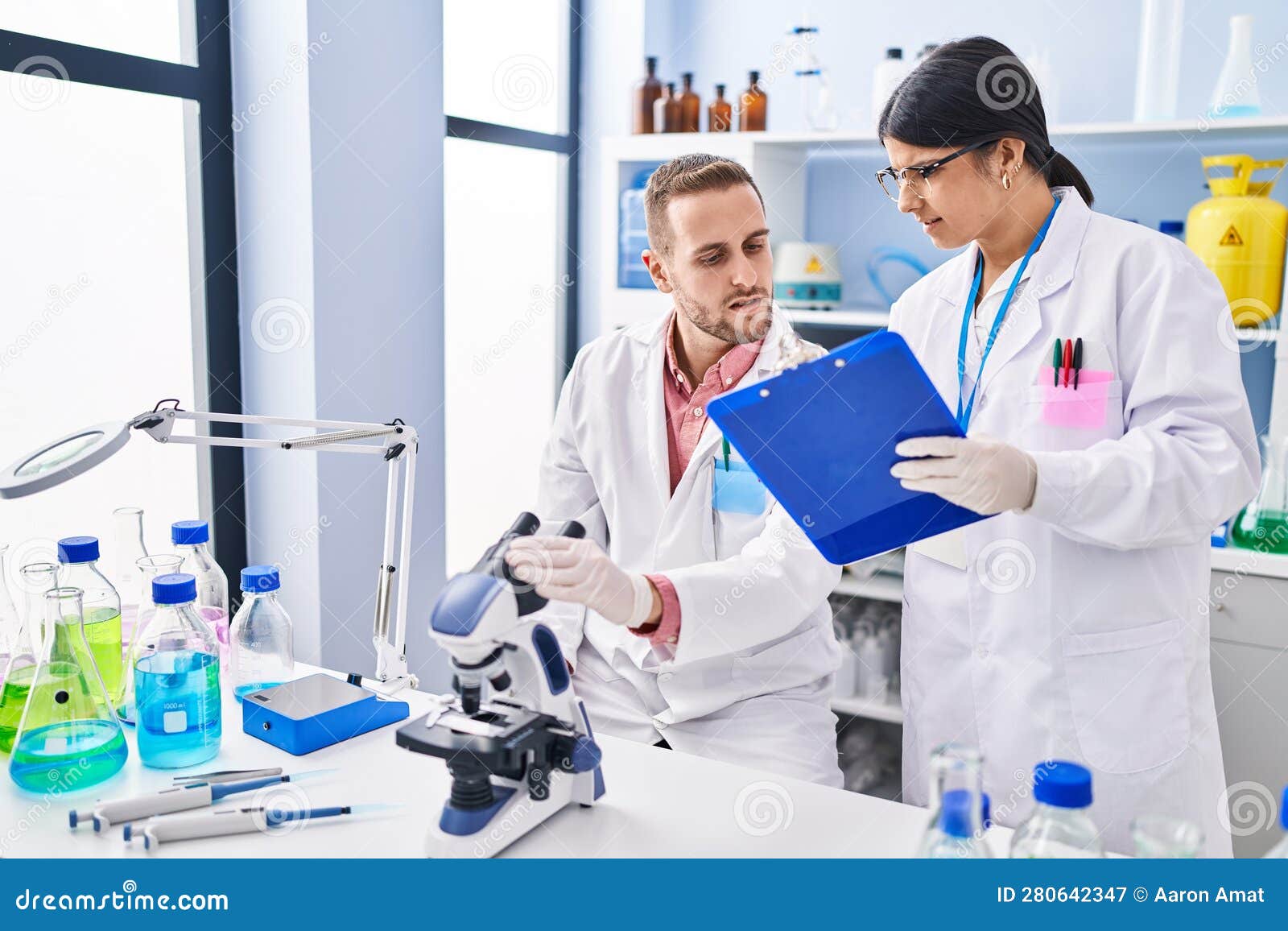 Man and Woman Wearing Scientists Uniform Using Microscope at Laboratory ...