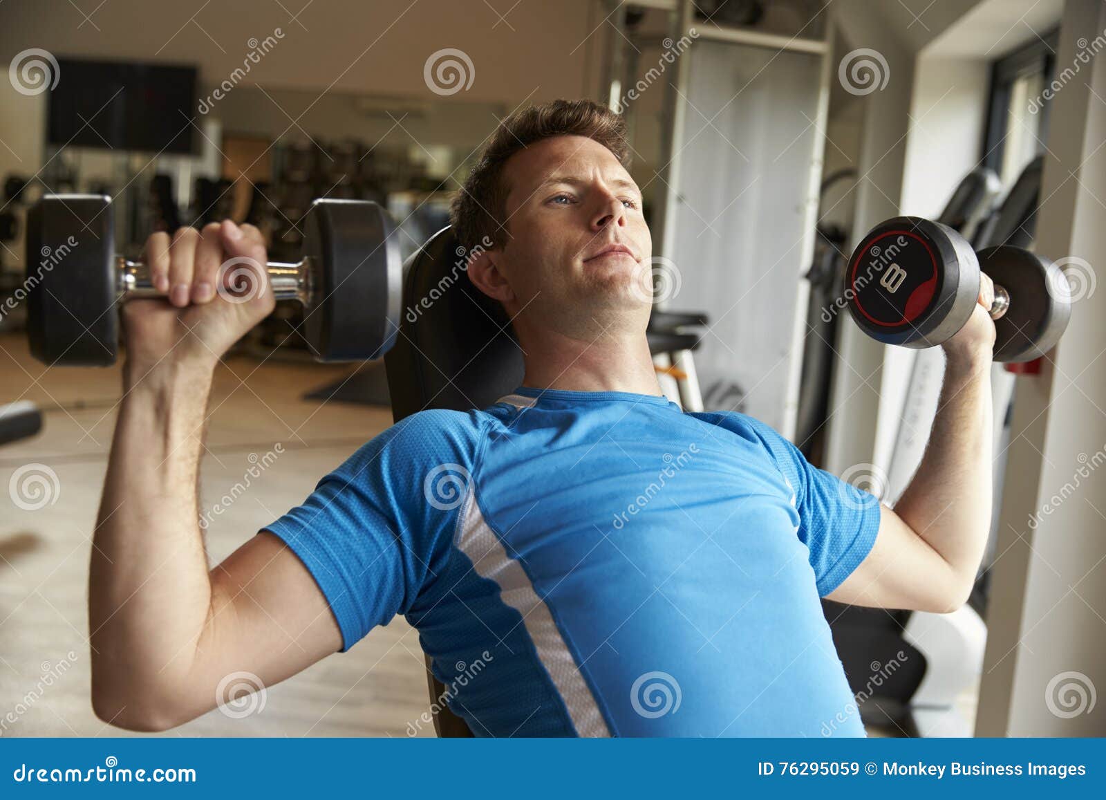 Man Works Out with Dumbbells on a Bench at a Gym, Front View Stock ...