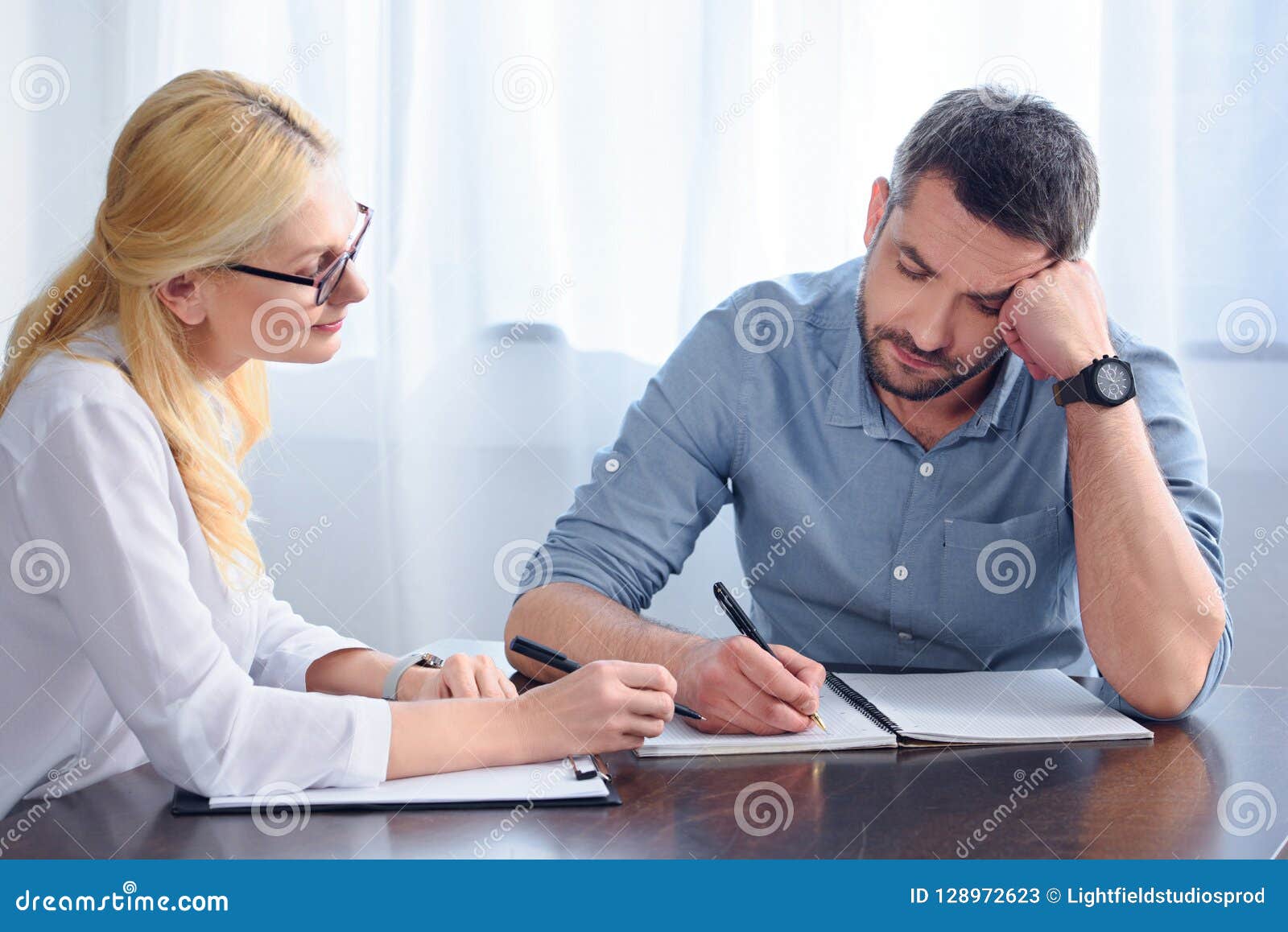 Man Writing Down in Empty Textbook while Sitting at Table Near Female ...