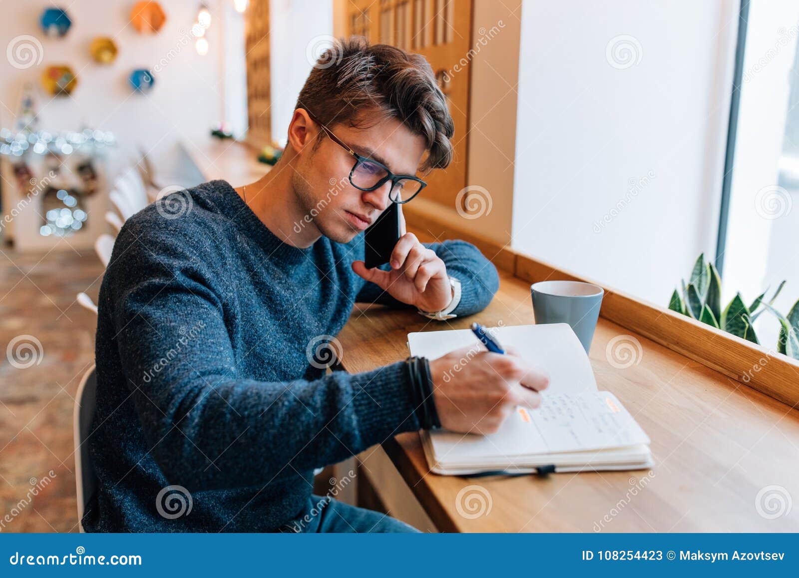 Man Writing Down Something in Notebook while Talking on Mobile Phone at ...