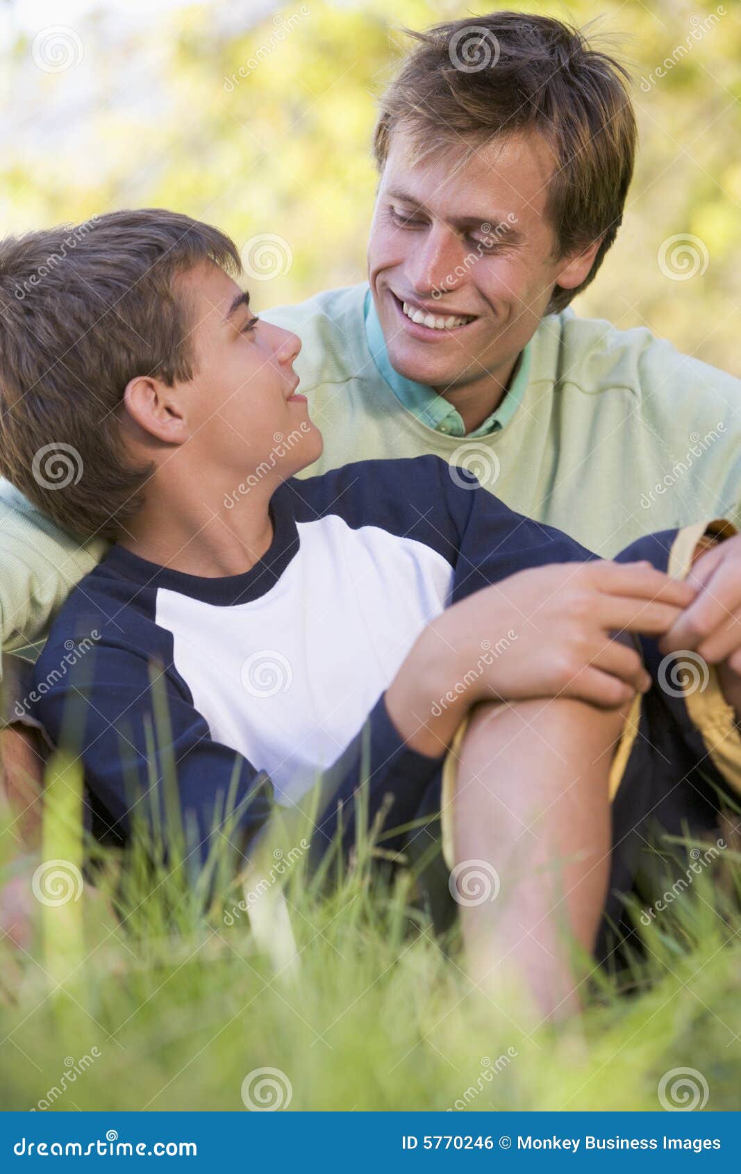 Man and Young Boy Sitting Outdoors Smiling Stock Photo - Image of field ...