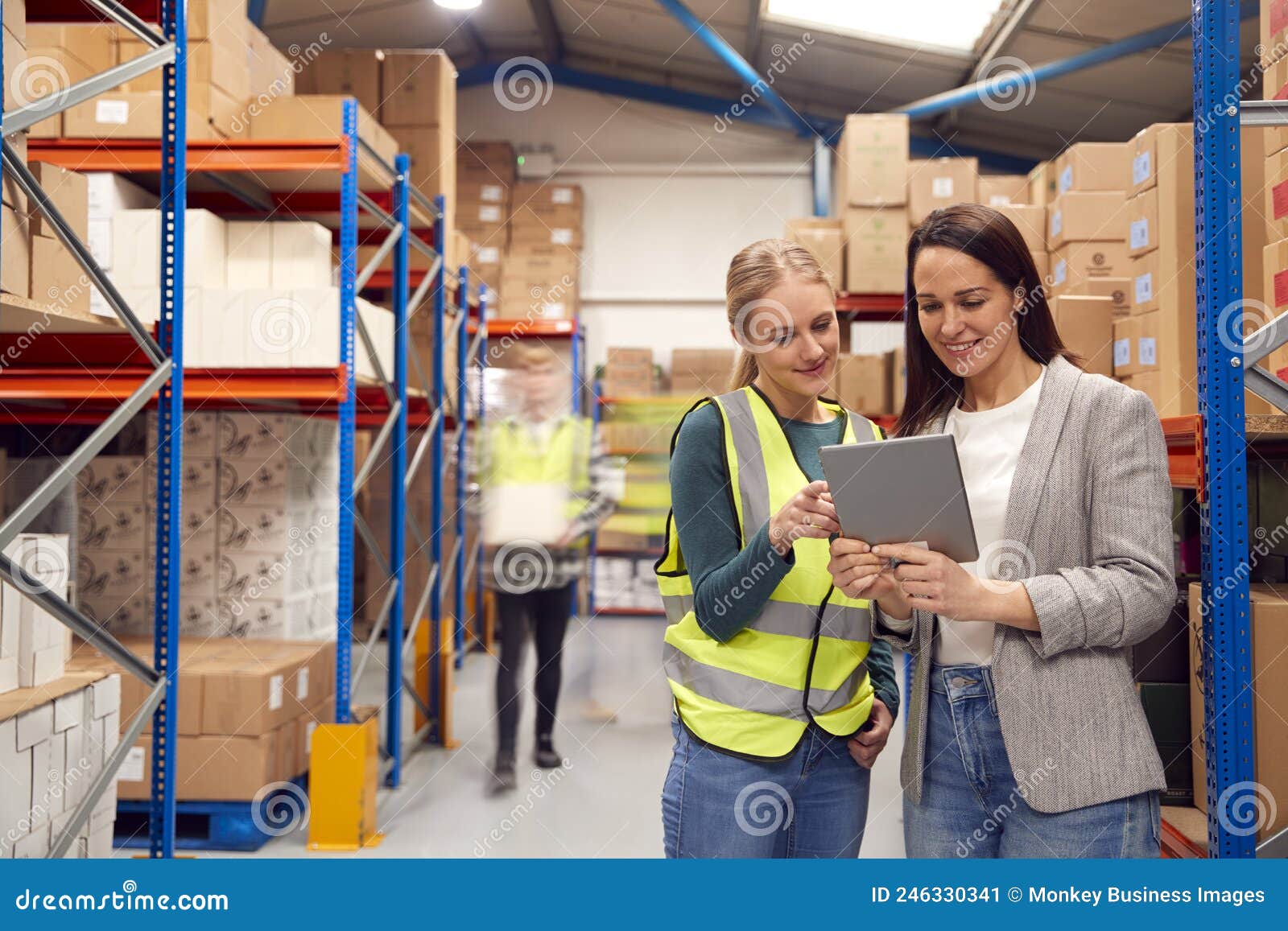 Manager Using Digital Tablet with Female Intern Inside Busy Warehouse ...