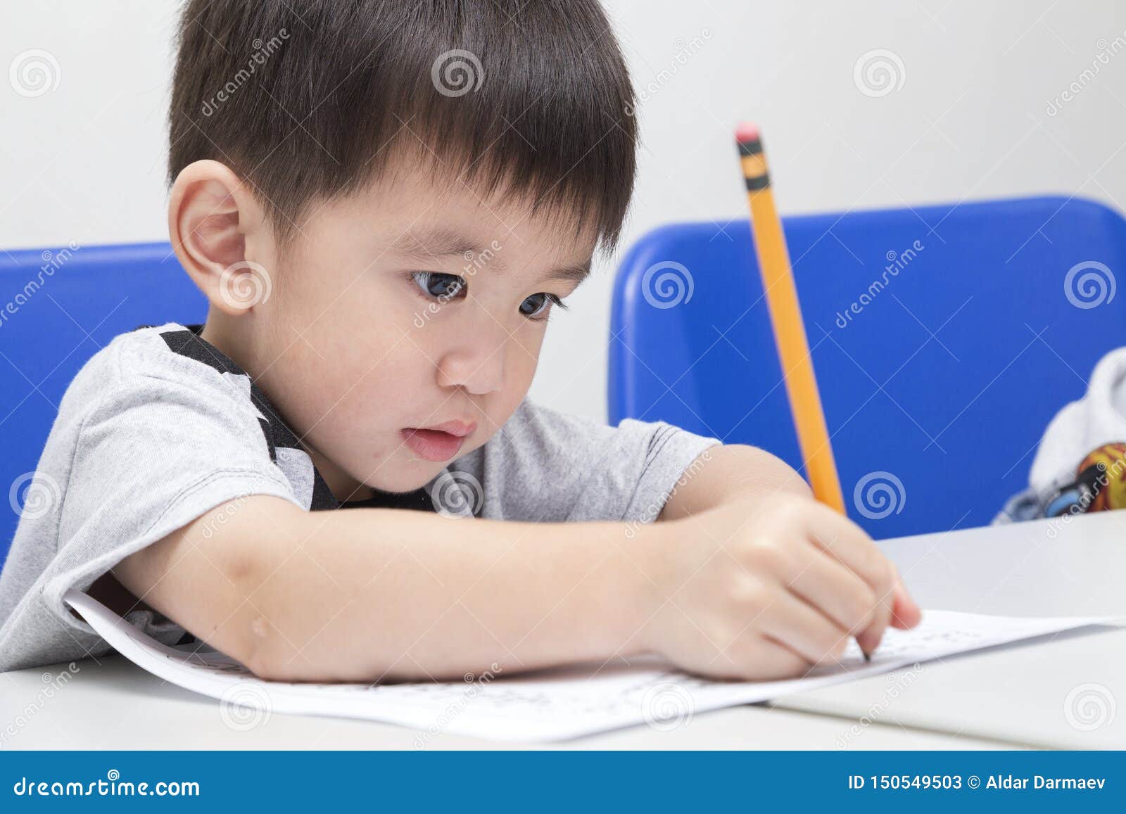 Little Boy is Learning To Write with a Pencil in Classroom at School ...