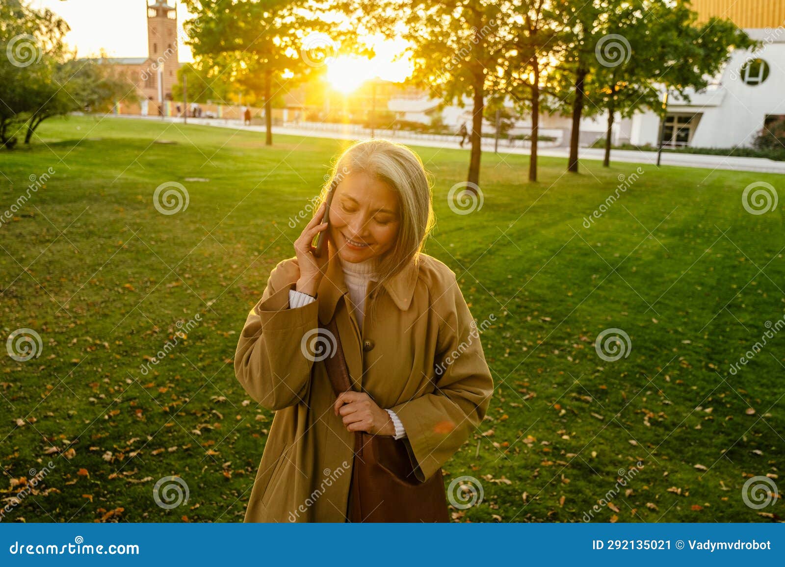 Mature Asian Woman Talking On Mobile Phone While Strolling In Park