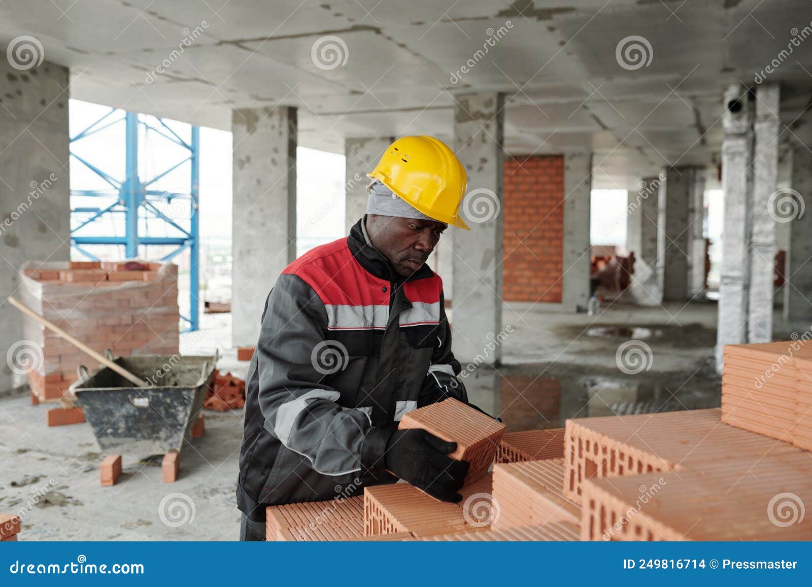 Mature Black Man in Workwear and Protective Helmet Putting Bricks in ...