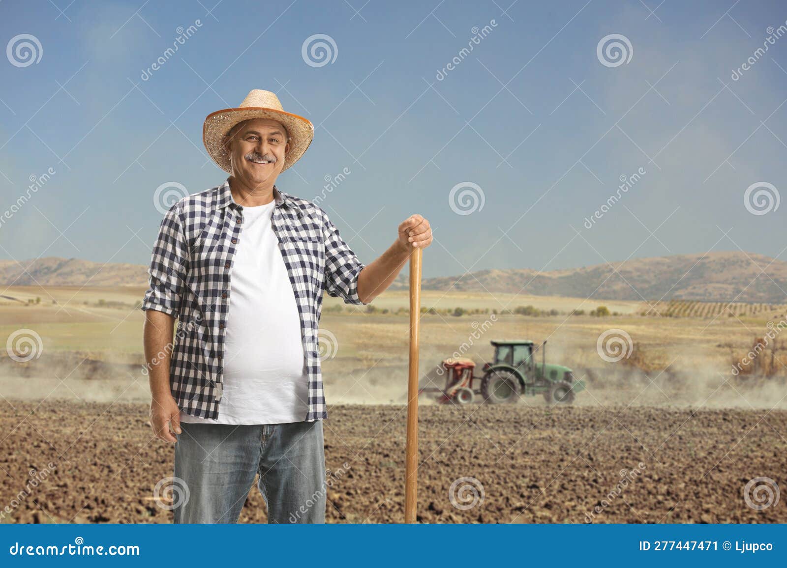 Mature Farmer with a Shovel Posing on a Field with a Tractor Stock ...