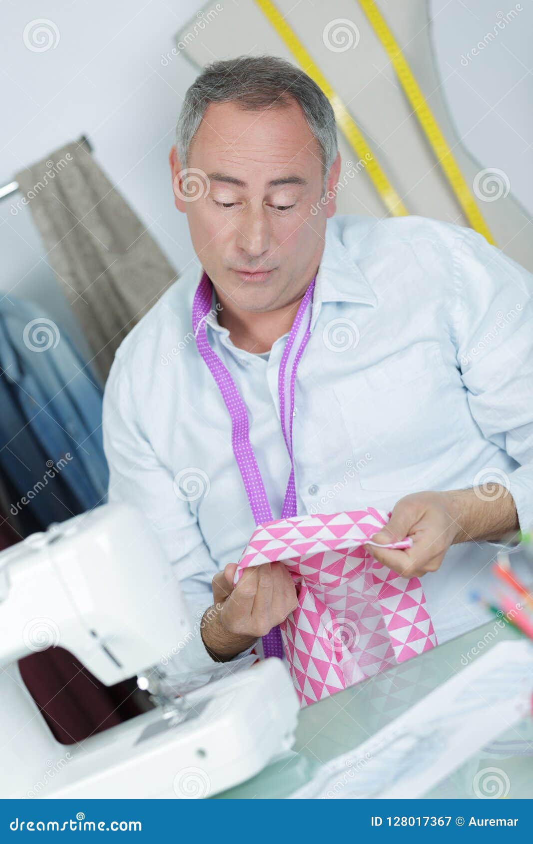 Male Dressmaker Stitching Cloth On Sewing Machine With Clothes Rack In ...